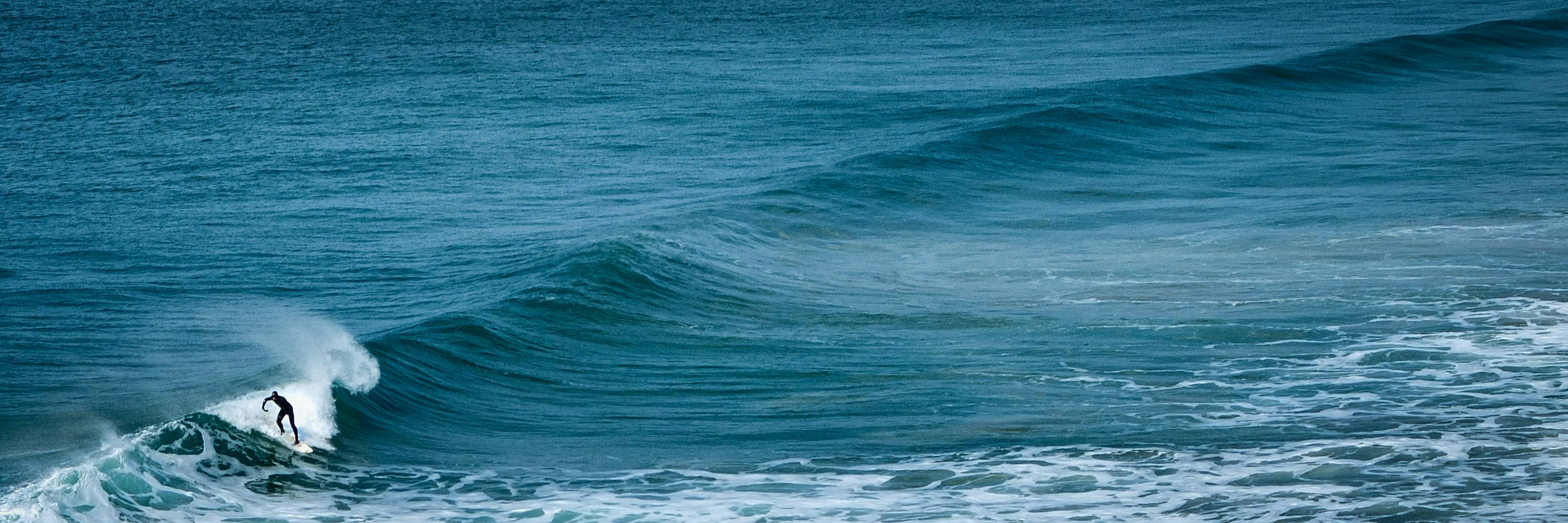 Chasing a Crest: A lone surfer on a rolling blue wall