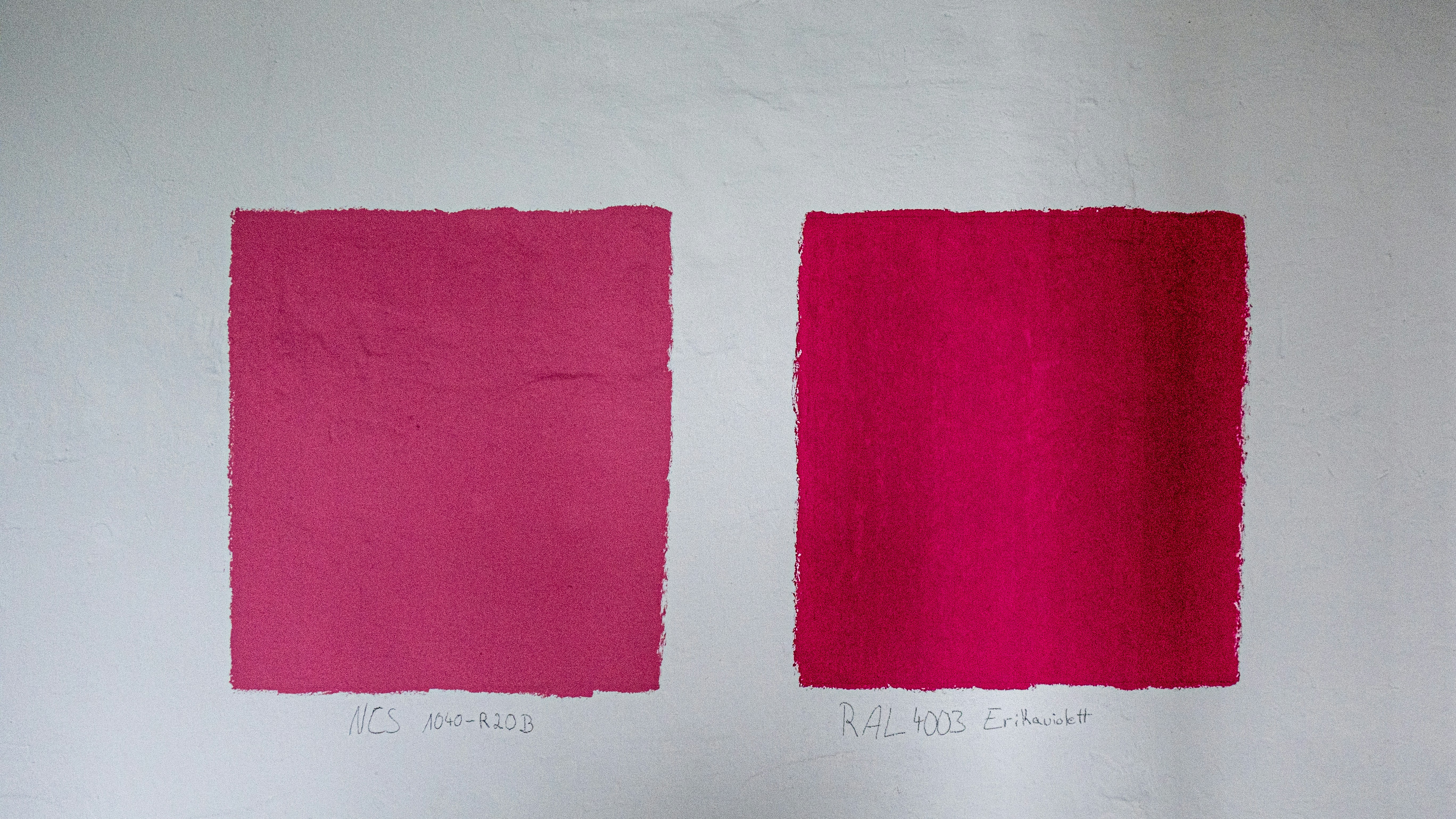 Two magenta color swatches mounted on a white wall, used for color reference.