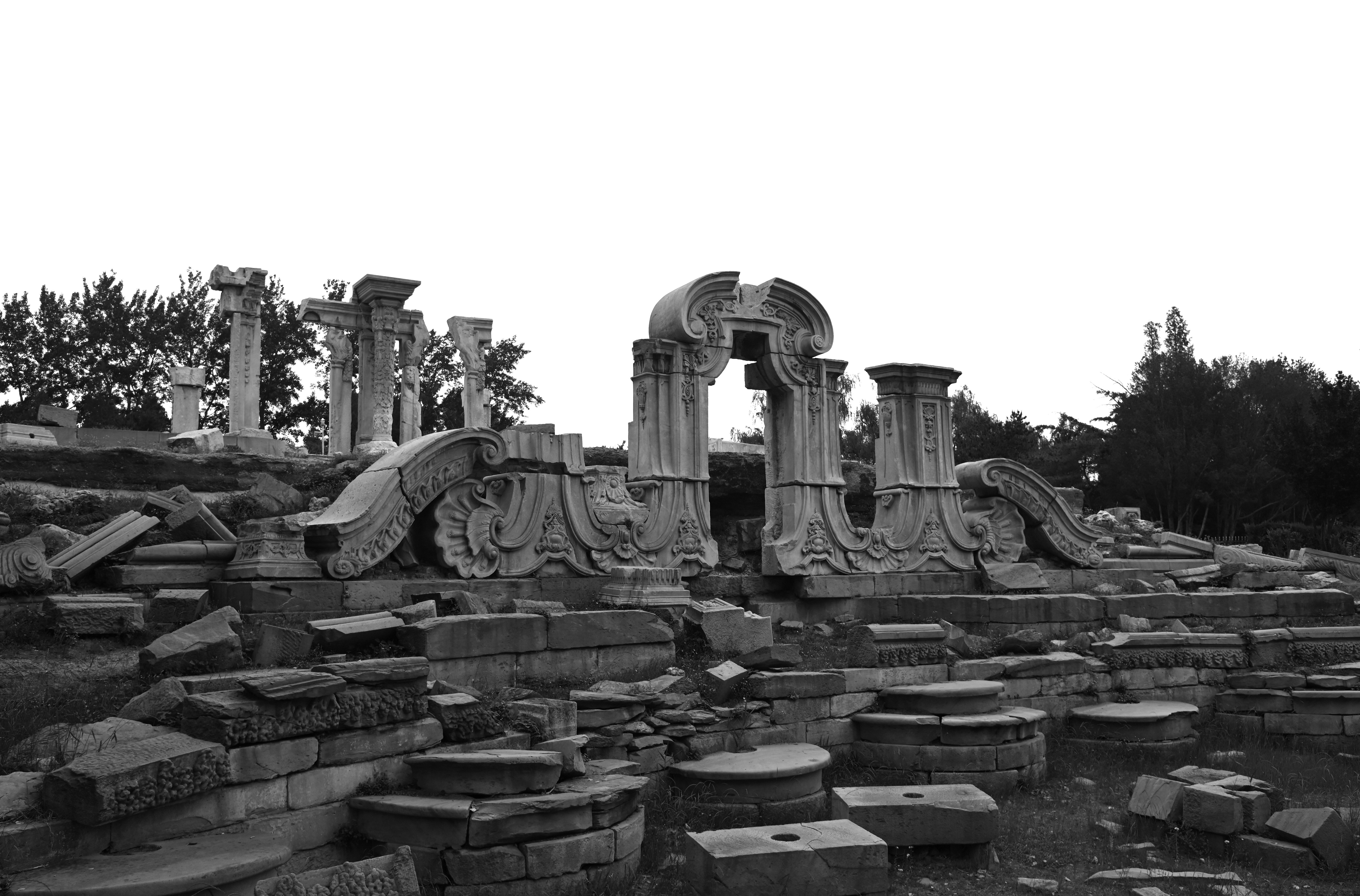 Ruins of classical architecture with intricately carved stone elements scattered across a landscape, highlighting the passage of time.