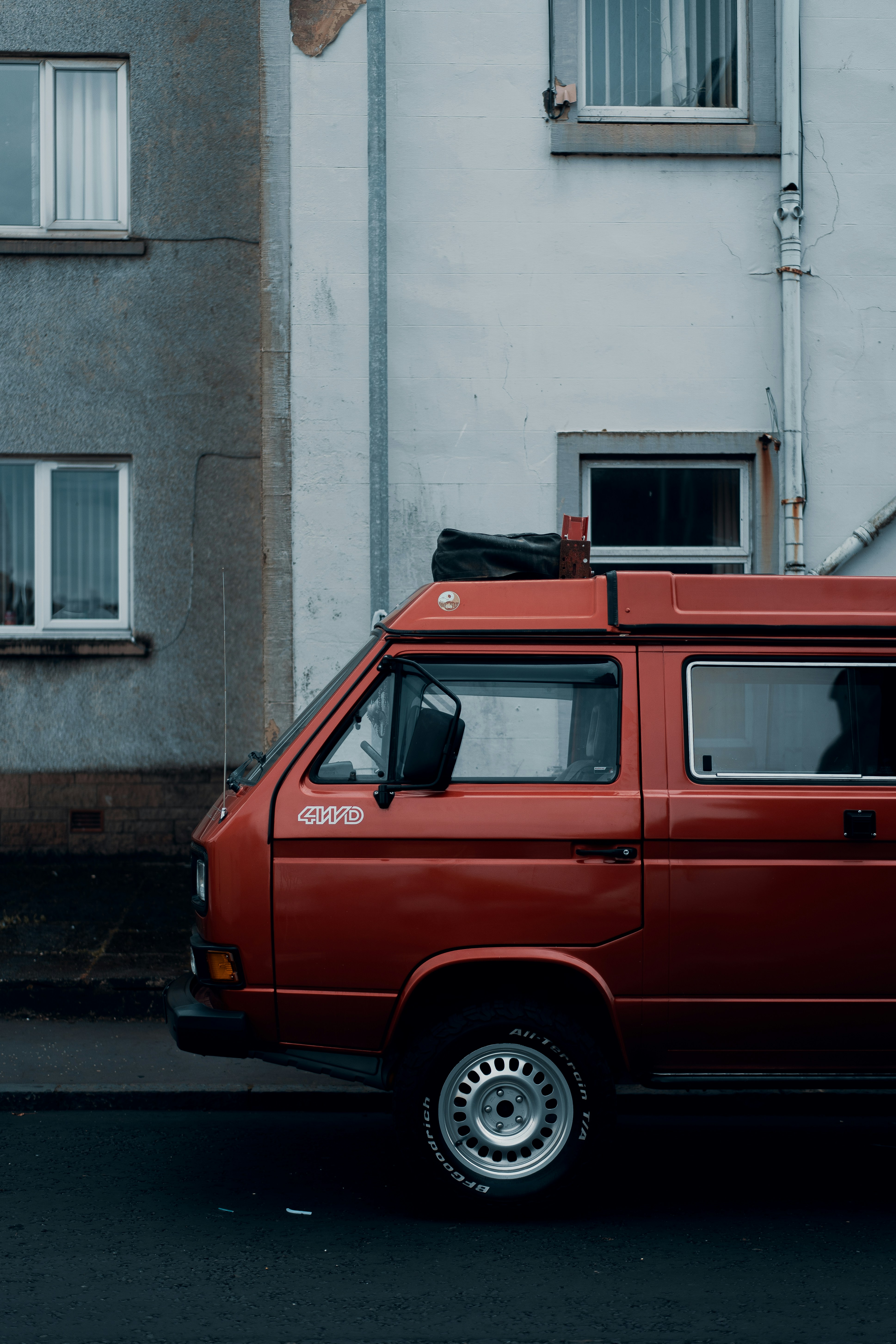 Side view of a vintage red van parked beside a textured wall, showcasing its distinctive design and character.
