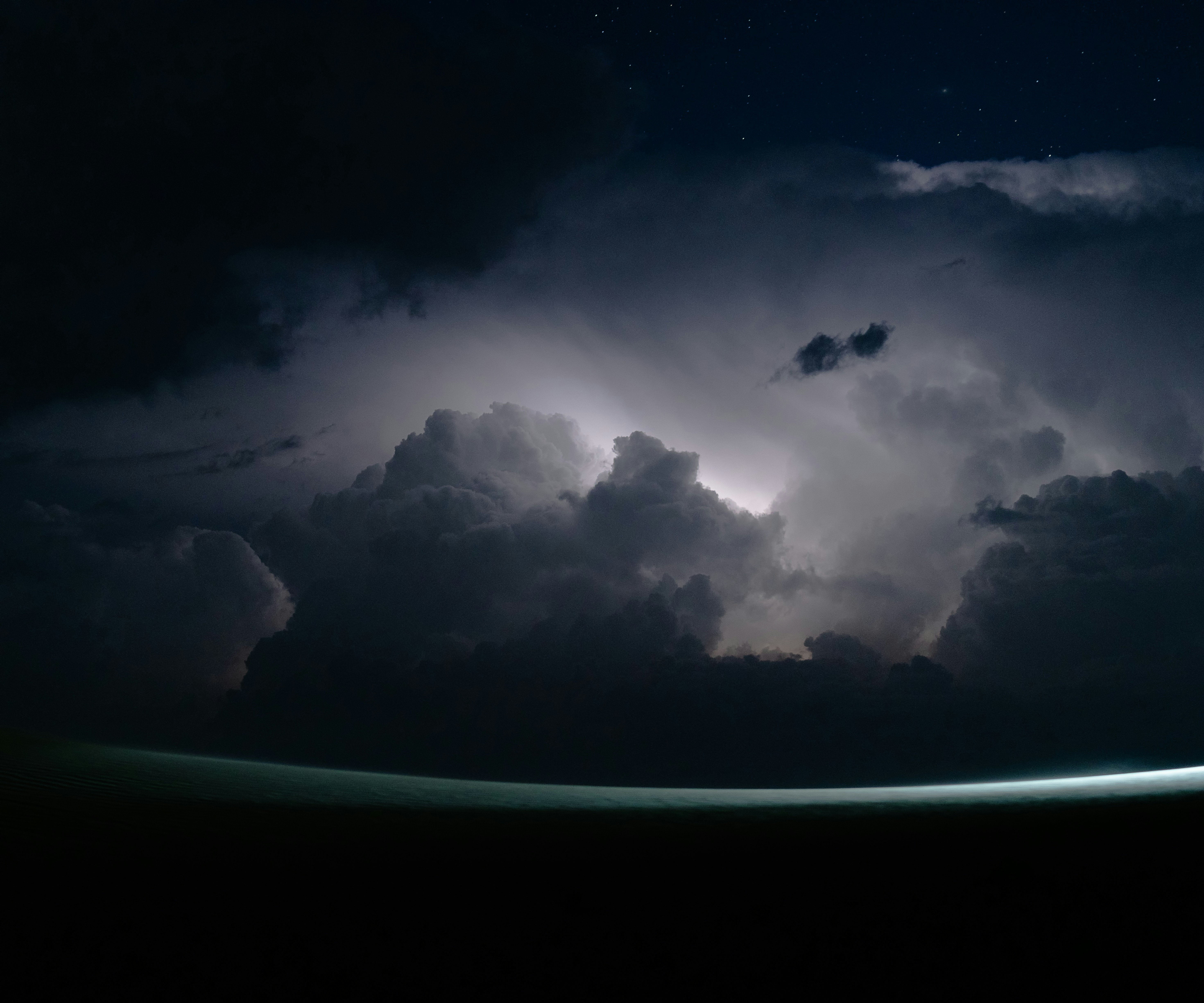 Dramatic lightning illuminating a dense cloud formation beneath a starry sky, creating a powerful atmospheric scene.