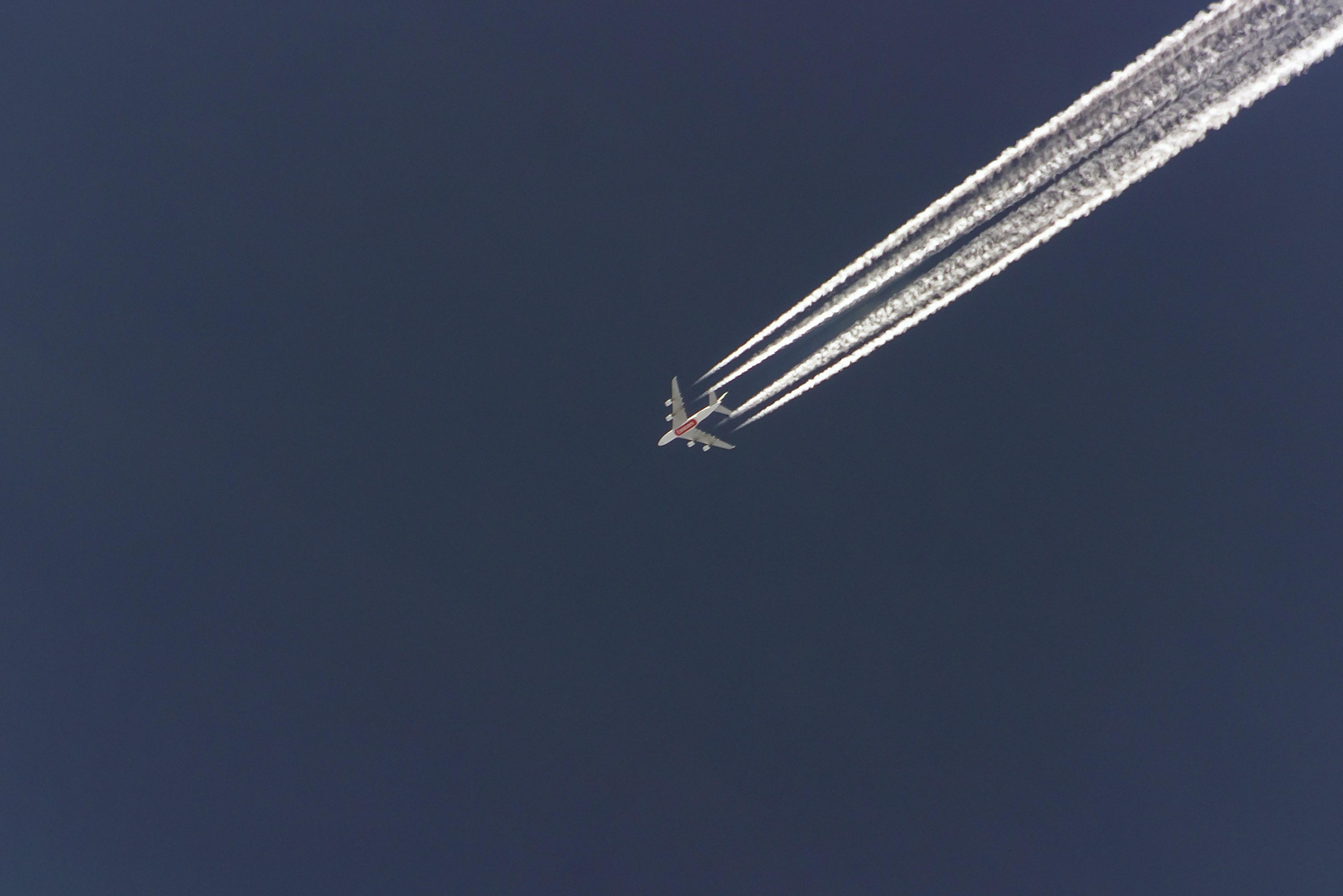 Commercial airplane soaring through a clear blue sky, leaving behind distinct contrails that trace its flight path.