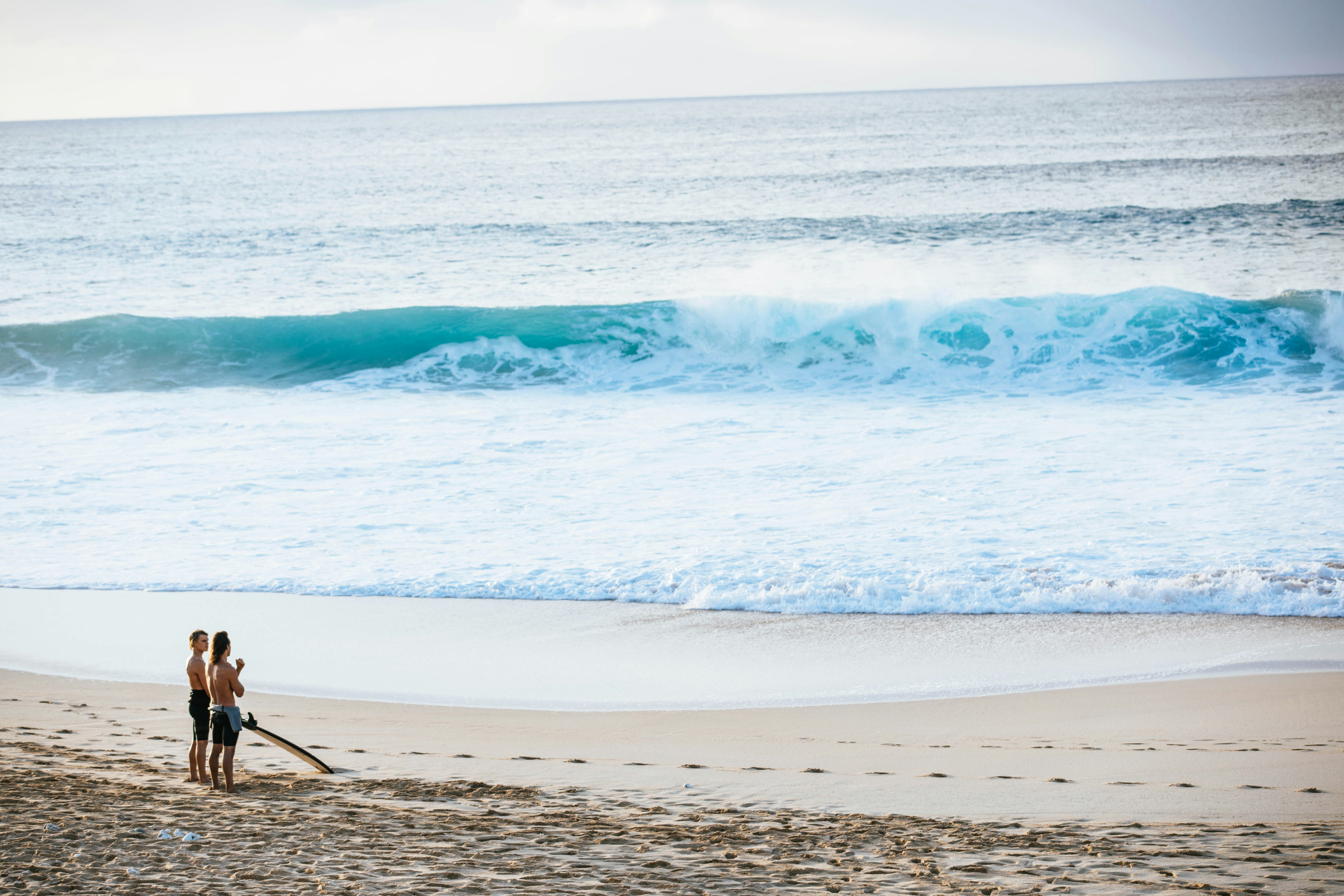 Person in black shorts walking along a sandy beach with rolling waves in the background.