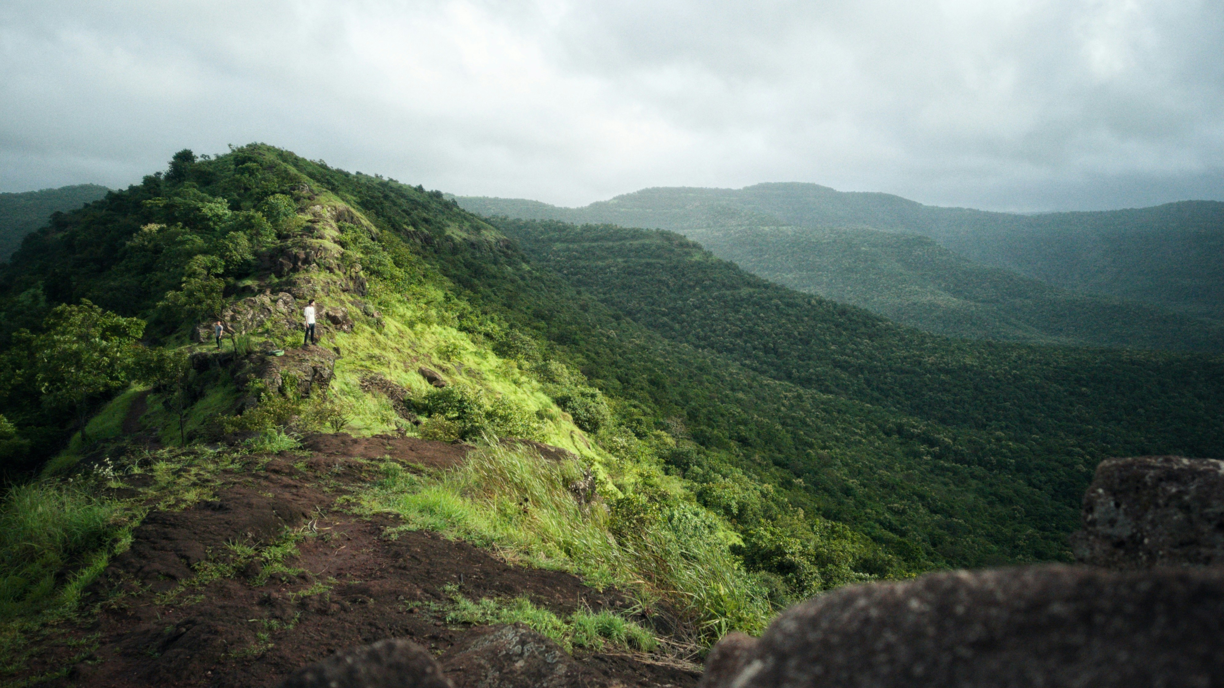 Lush green mountain ridge with hikers under a dramatic cloudy sky.