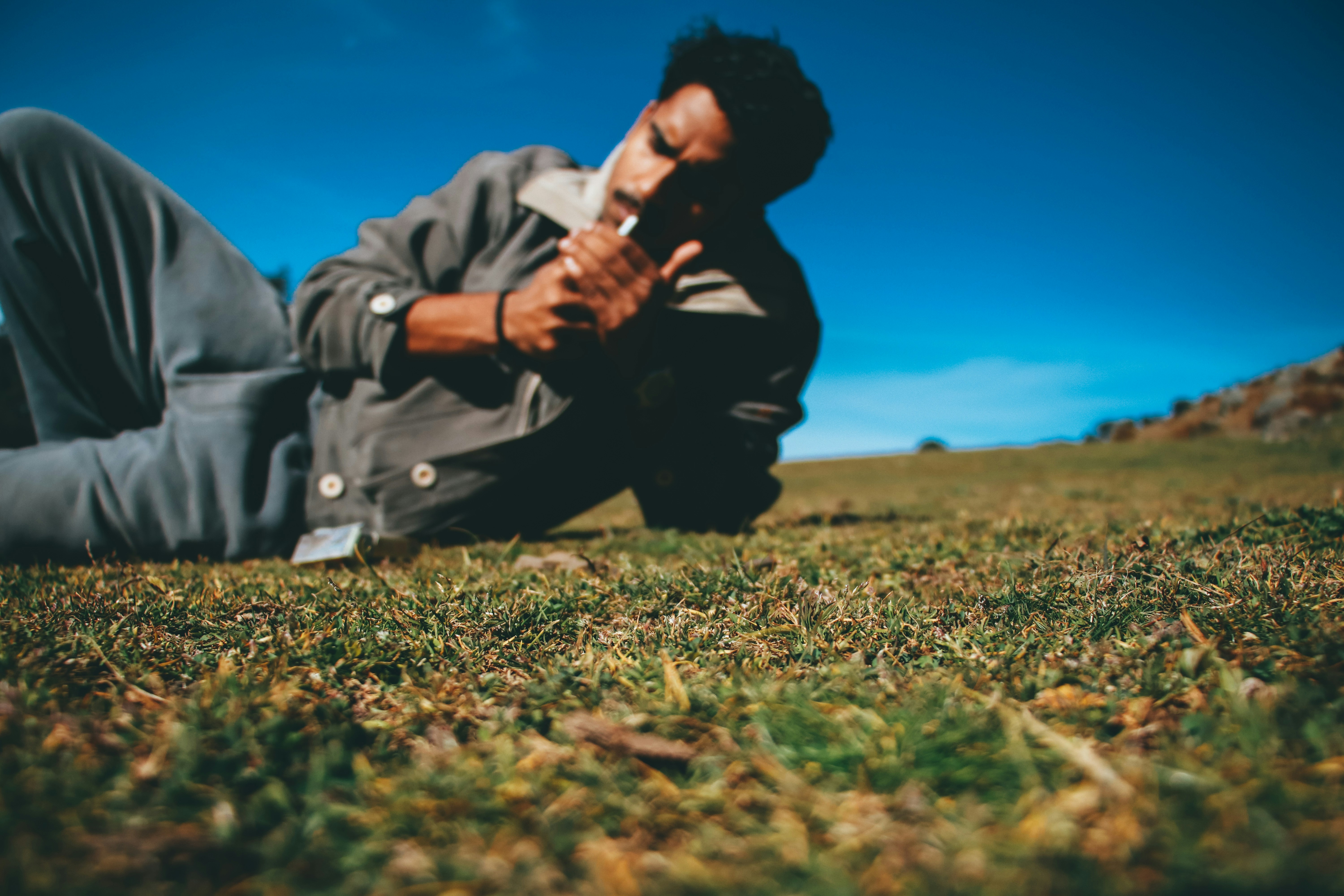 Person lying on grass under a clear blue sky, deeply engaged with a smartphone.