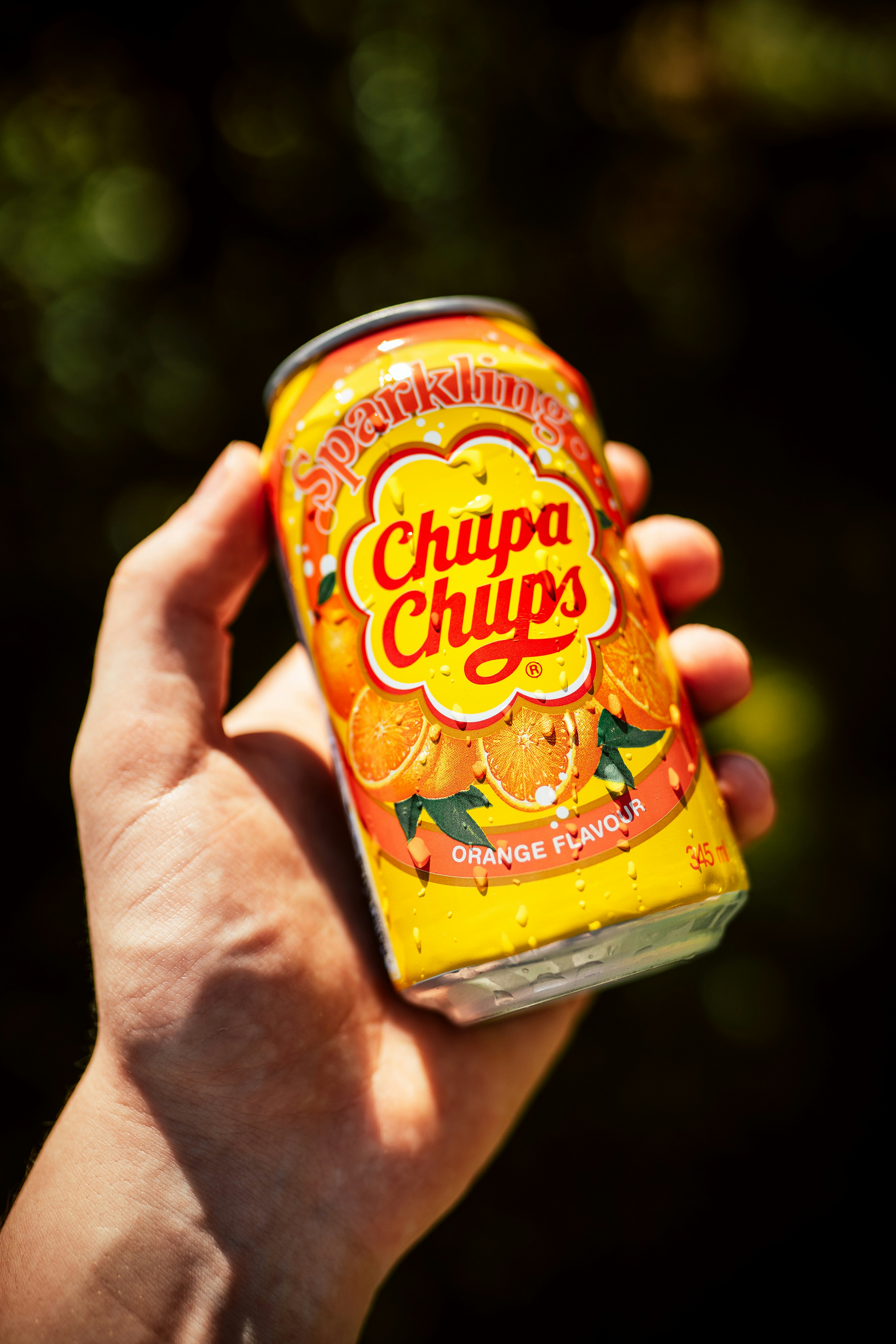 Handheld Citrus Burst: Chupa Chups Sparkling Orange Can in Sunlit Focus