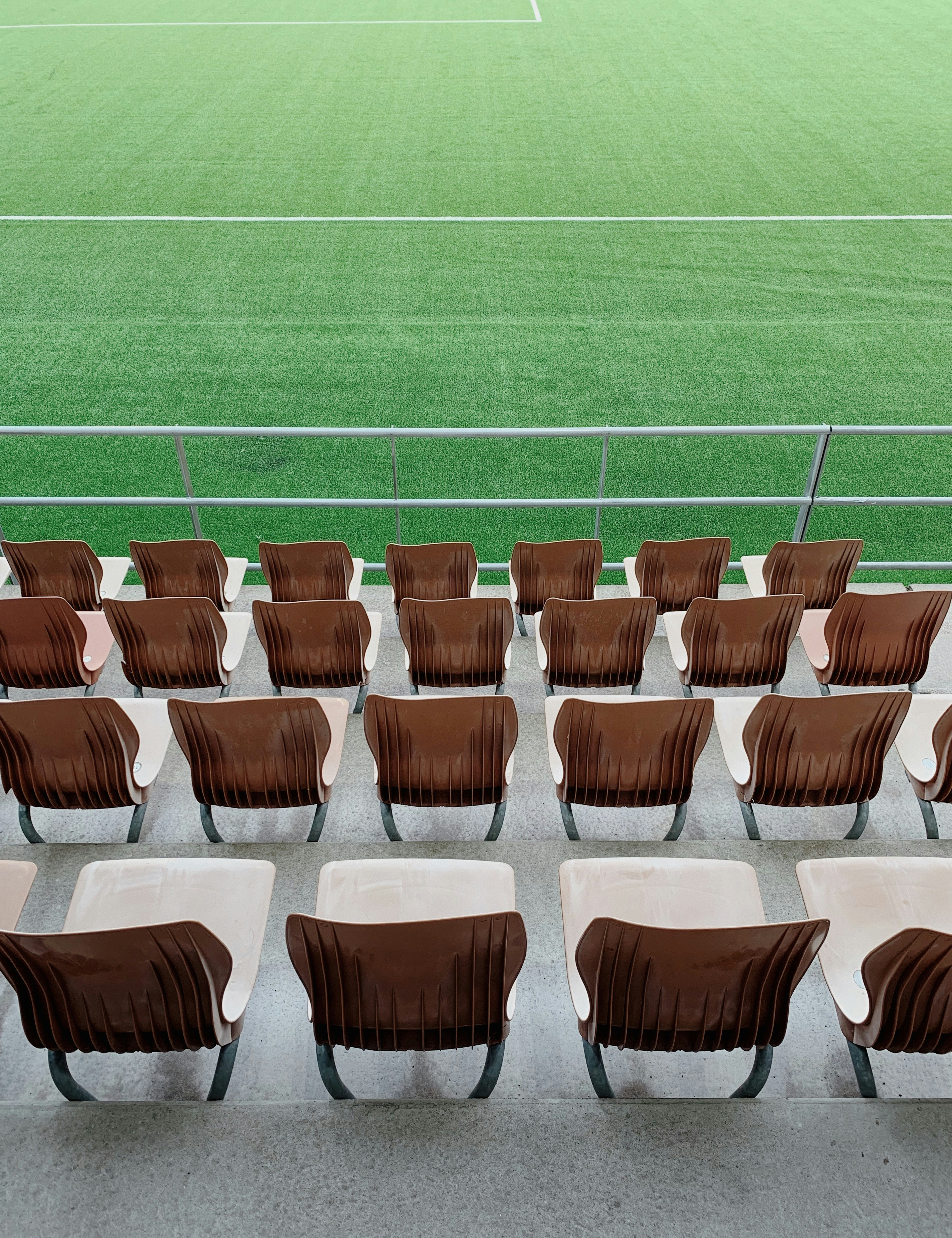 Rows of brown and beige stadium seats overlook a lush green soccer field, emphasizing the anticipation of an upcoming match.