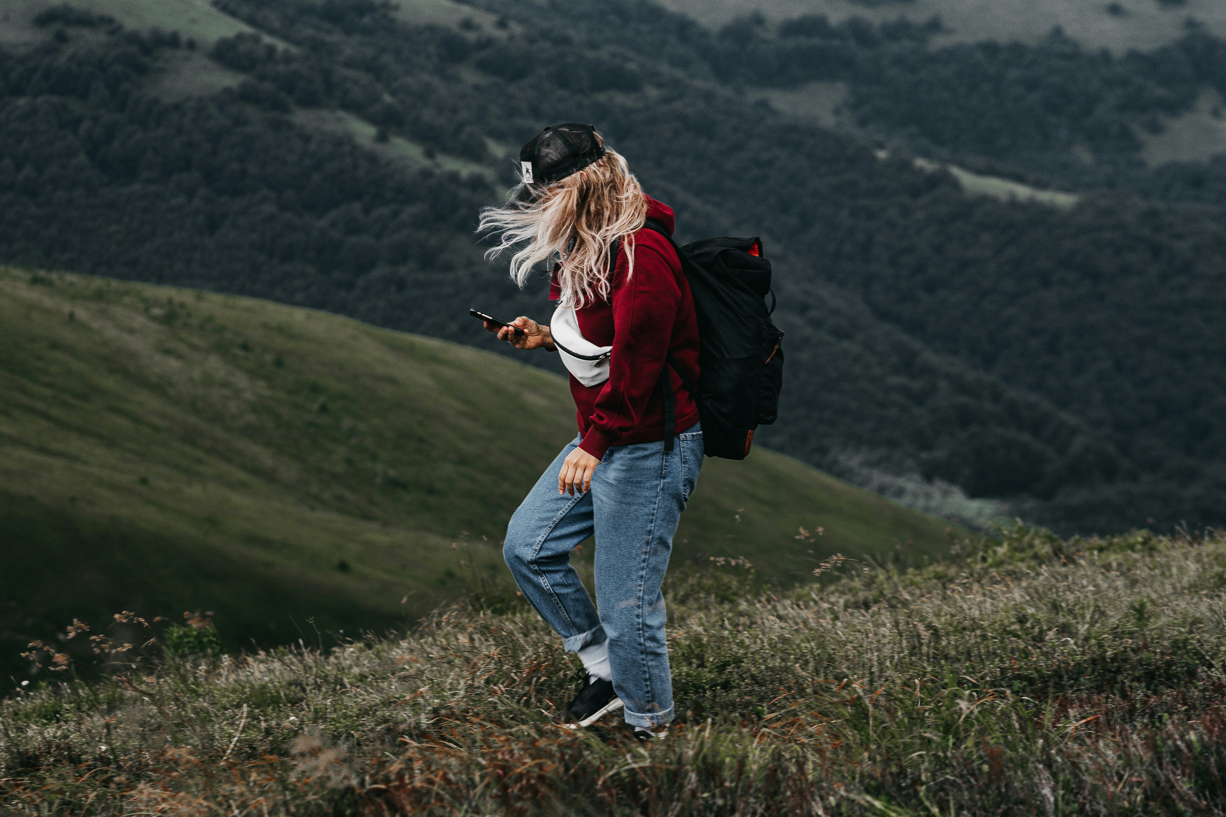 A person in casual attire navigates a hillside, absorbed in their phone amidst a lush green landscape. The scene captures the harmony between technology and nature.