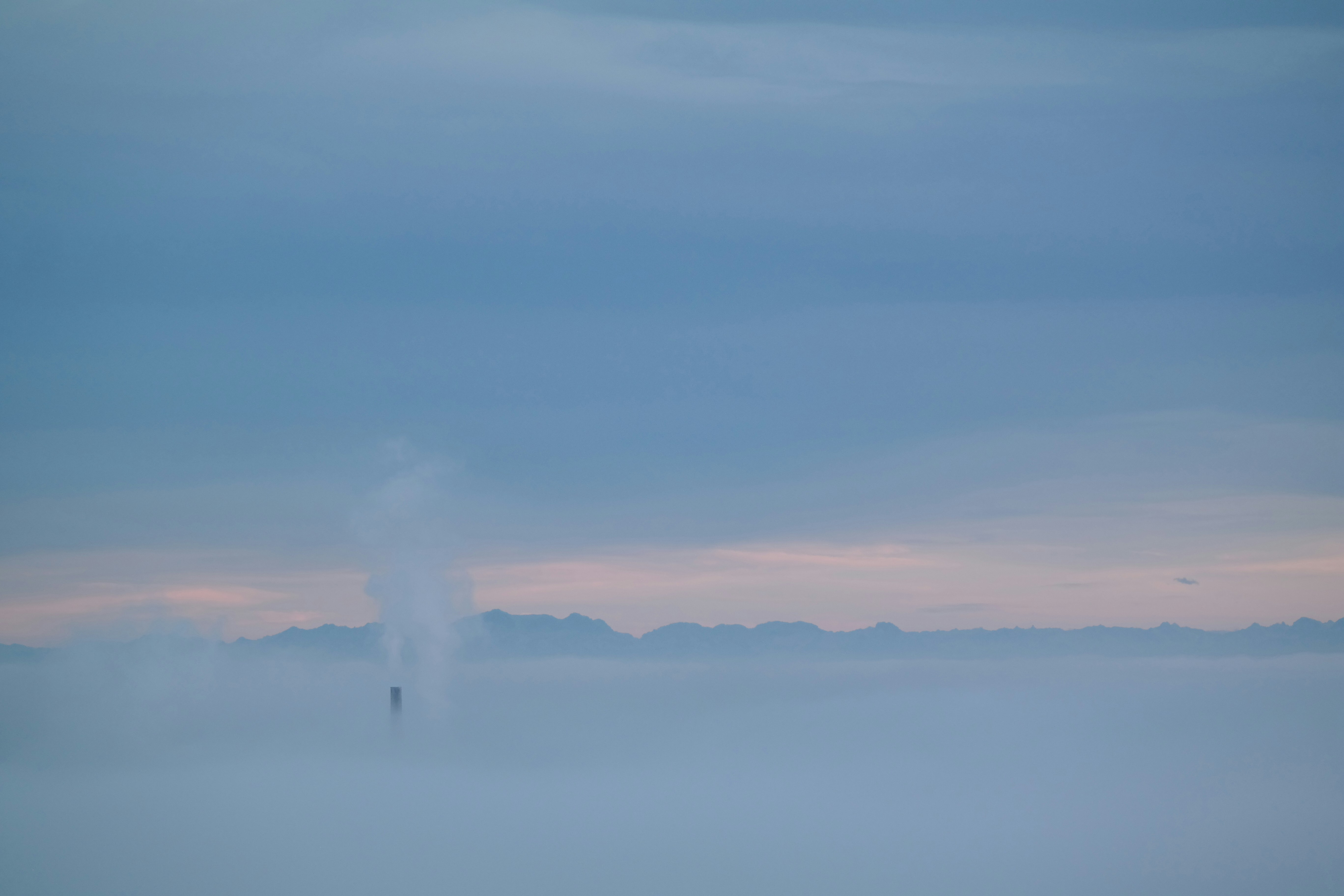 Soft clouds envelop a distant mountain range with a plume of vapor rising gently.