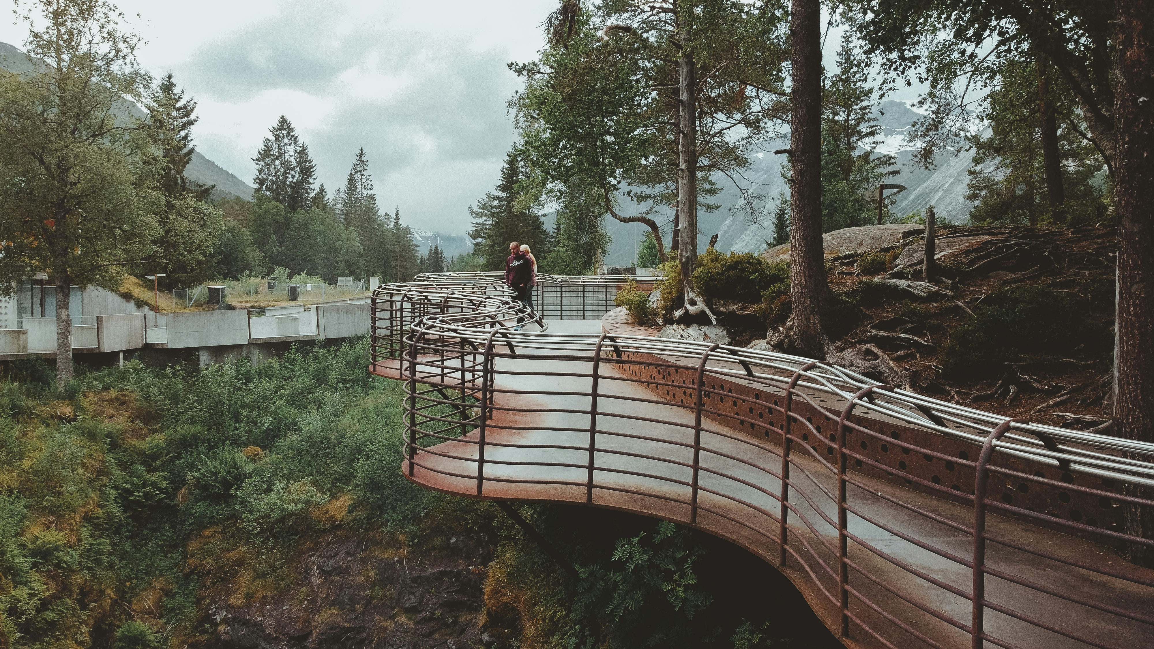 Couple sharing a moment on a wooden bridge surrounded by lush greenery and mountains. The scene conveys a sense of tranquility and connection with nature.