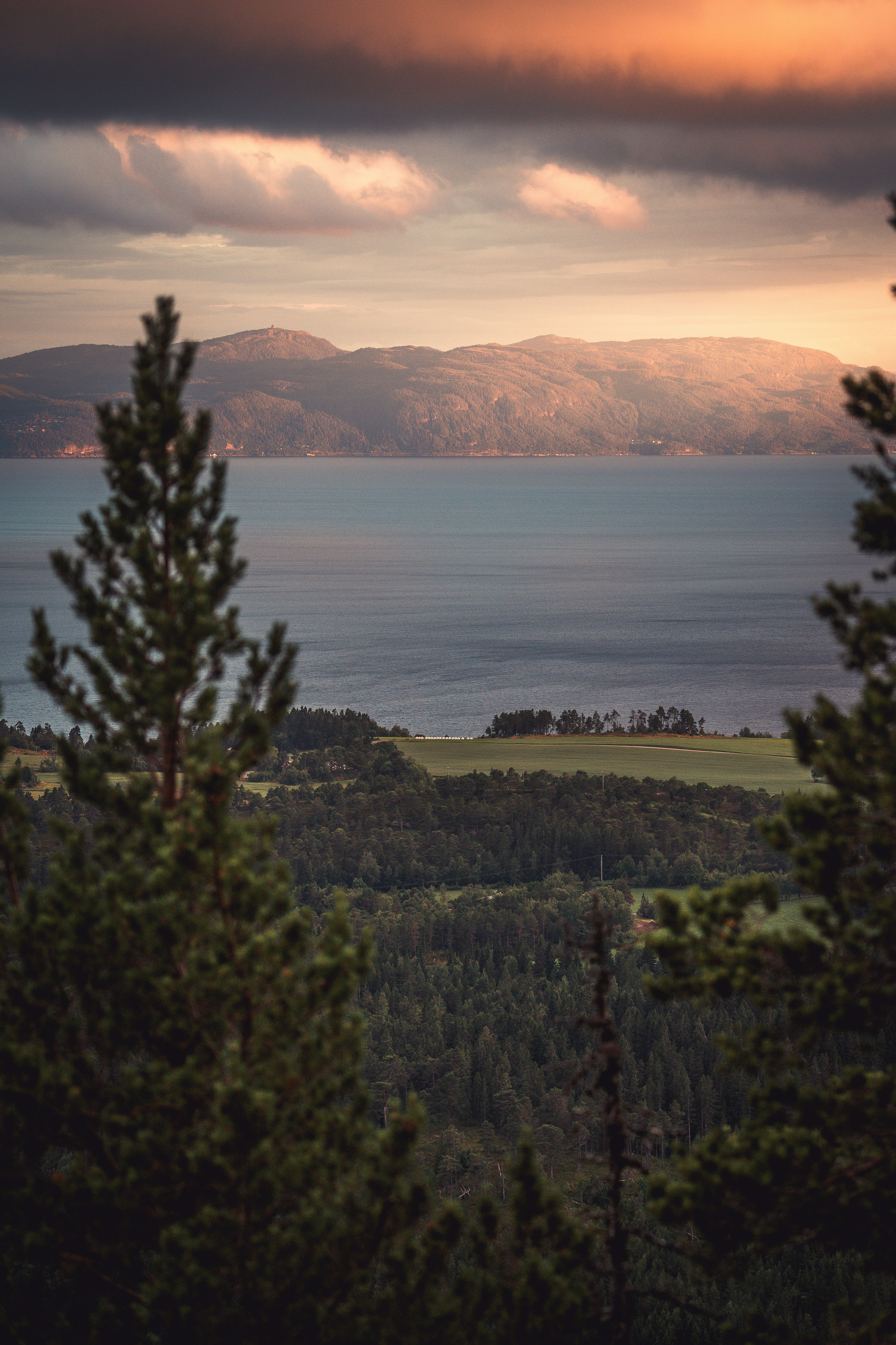 Coastal landscape with rolling hills and a calm sea under a dramatic sky at sunset.