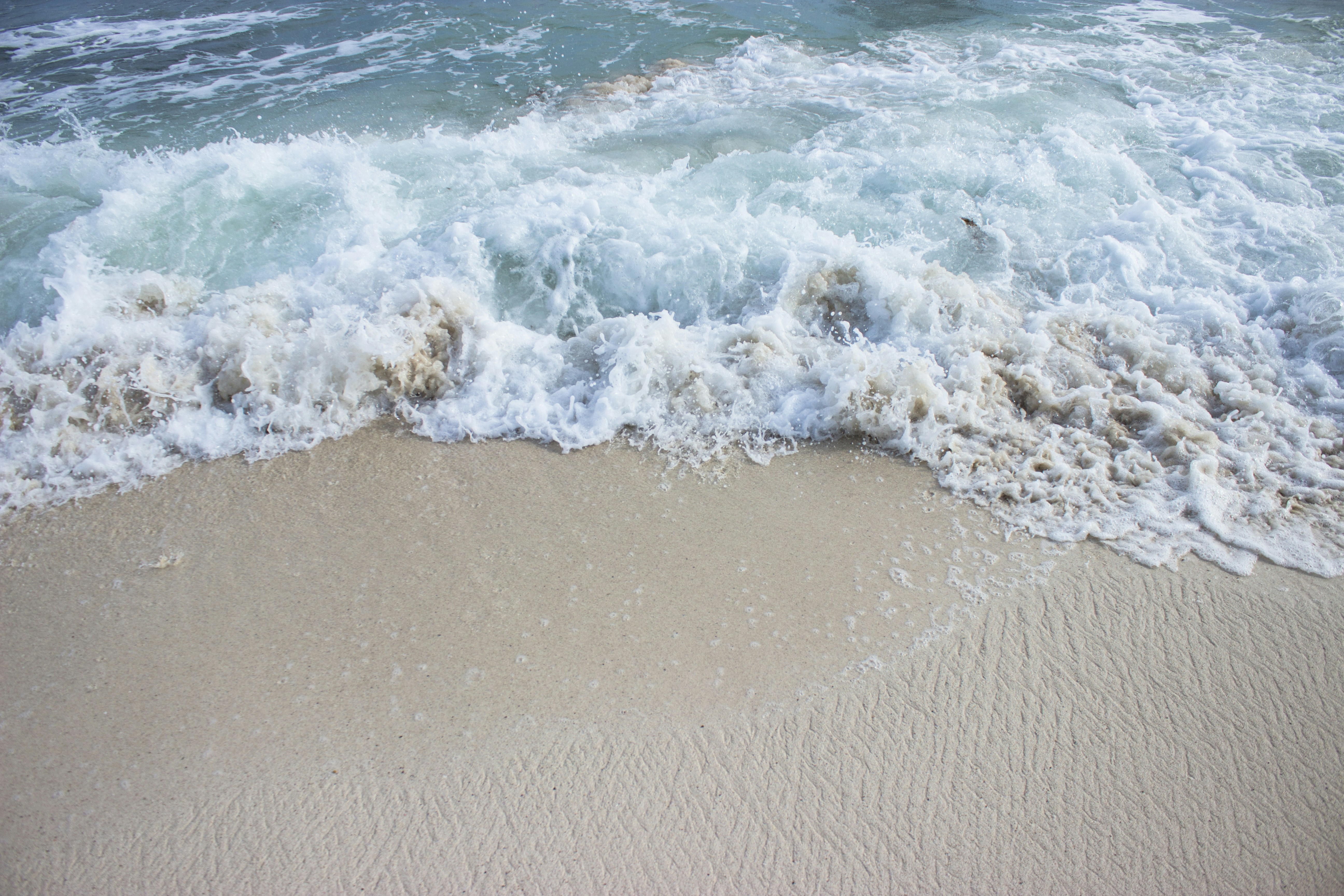 Waves gently wash over a sandy beach, blending textures of foam and smooth sand.