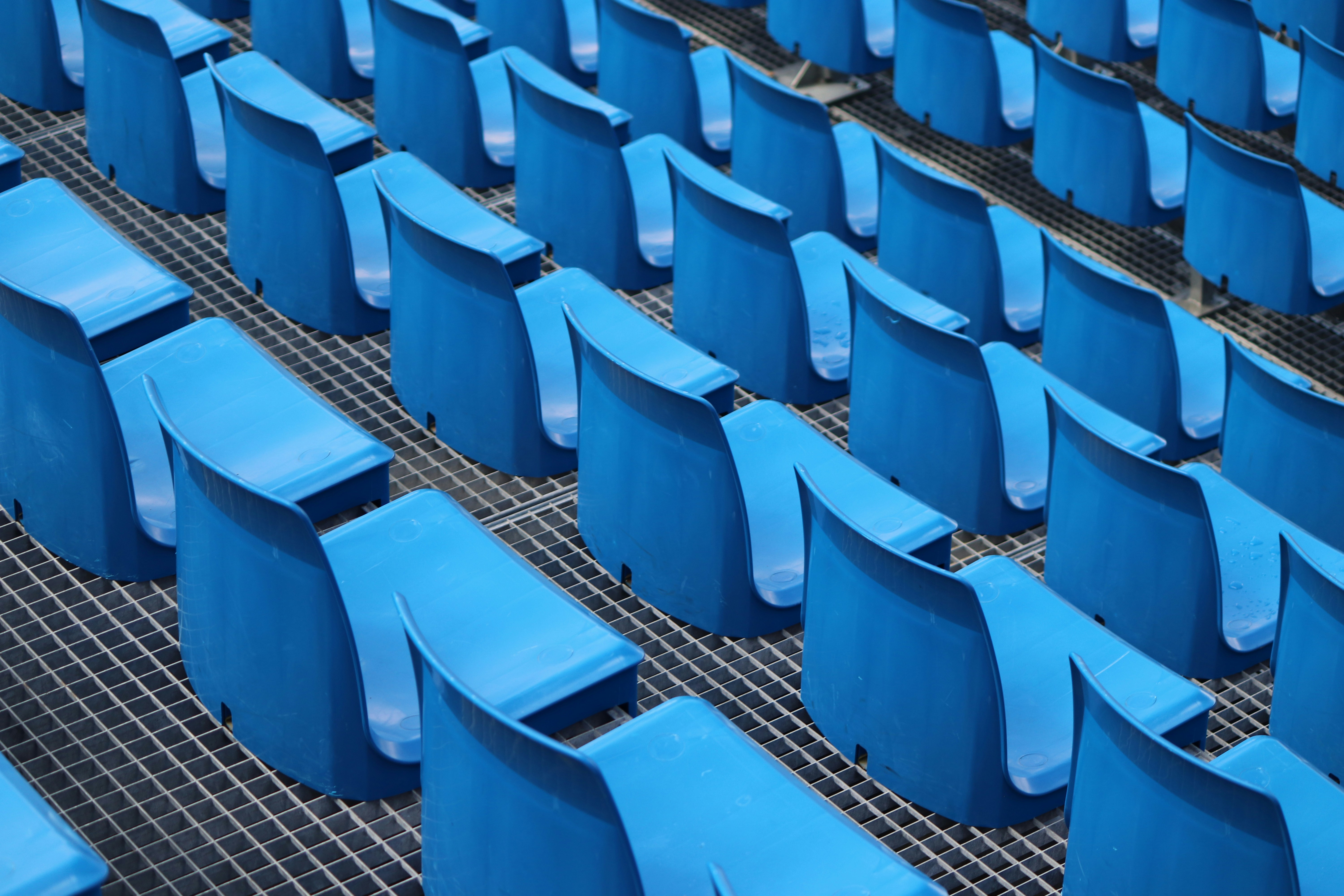 Rows of blue plastic seats arranged in a grid pattern, showcasing a vibrant and orderly design. The image emphasizes the emptiness and anticipation of an event yet to unfold.
