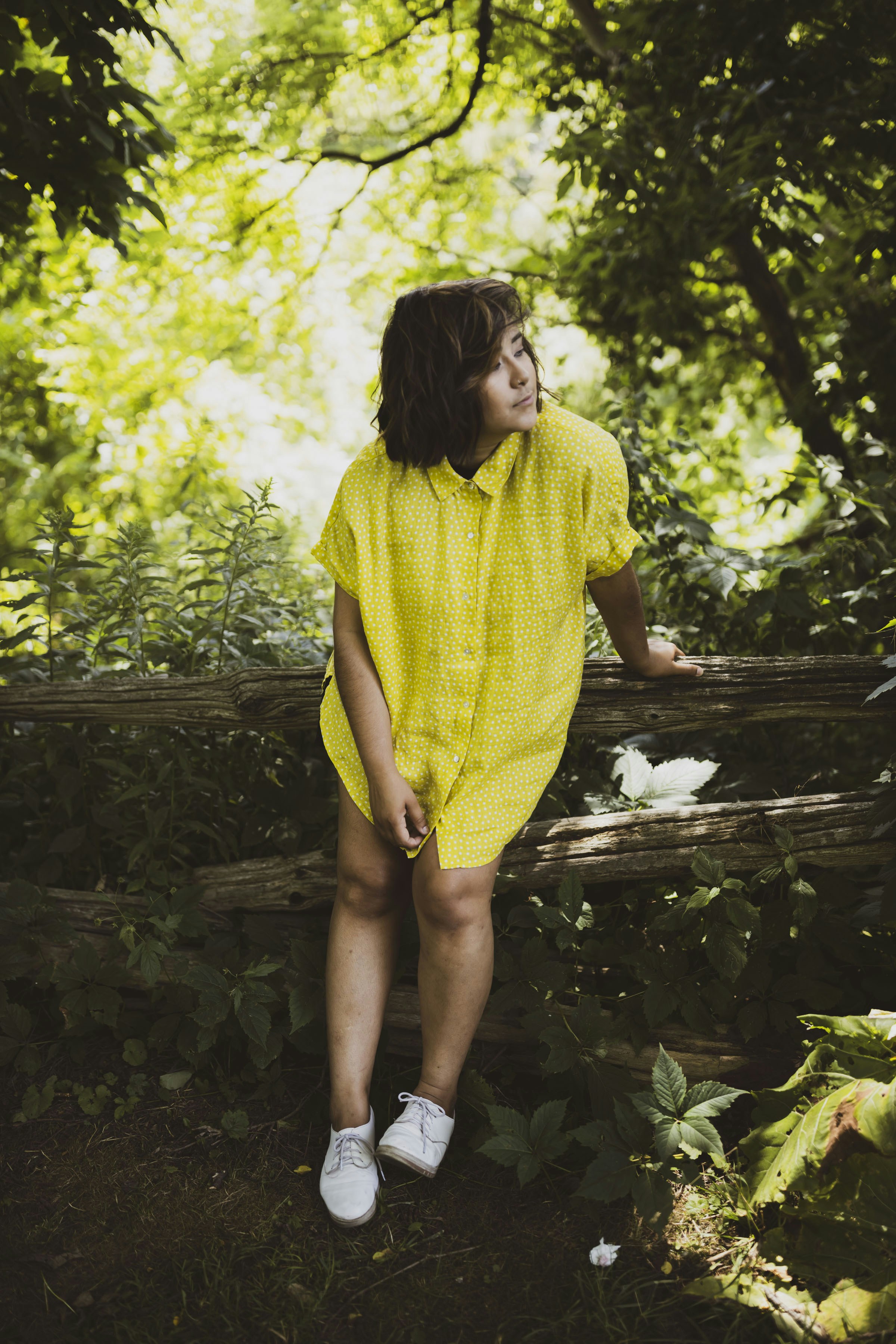 Yellow-dressed girl resting on a rustic fence in sunlit woods