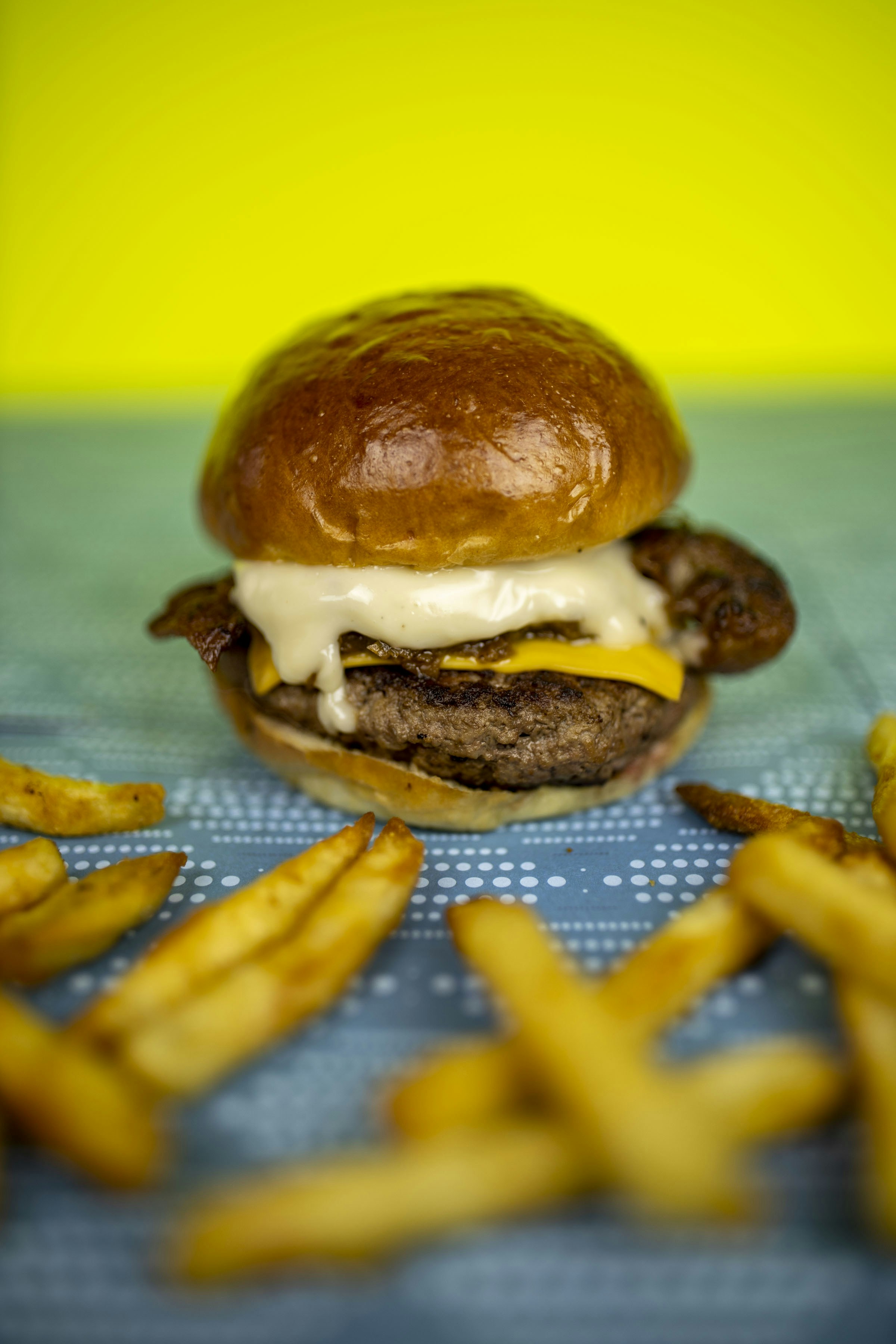 Center-Stage Cheeseburger: Gooey Cheese Meets Crunchy Fries Against a Bold Yellow Backdrop