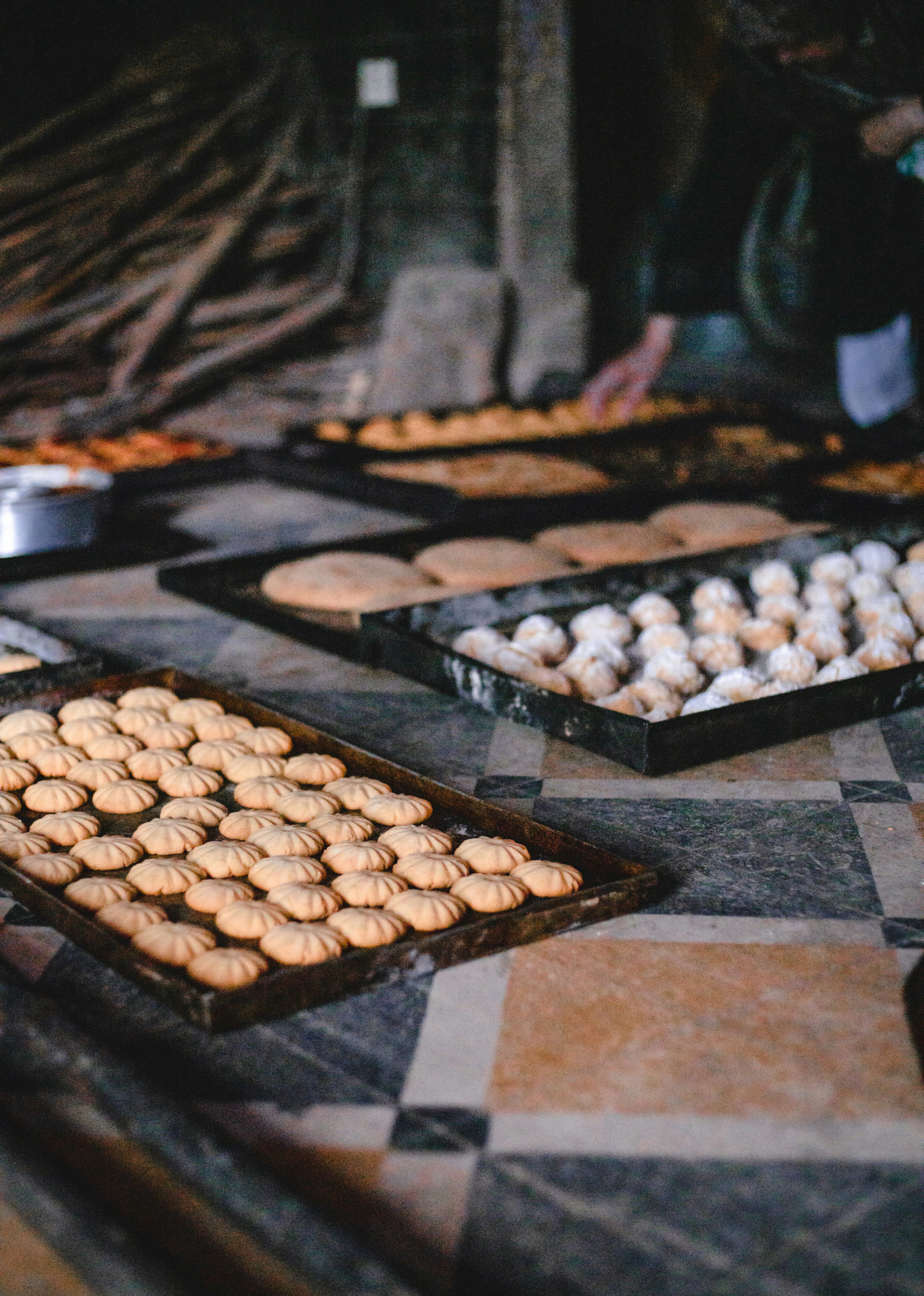 Trays of meticulously crafted pastries arranged on a patterned floor, showcasing the intricate details of traditional baking techniques.