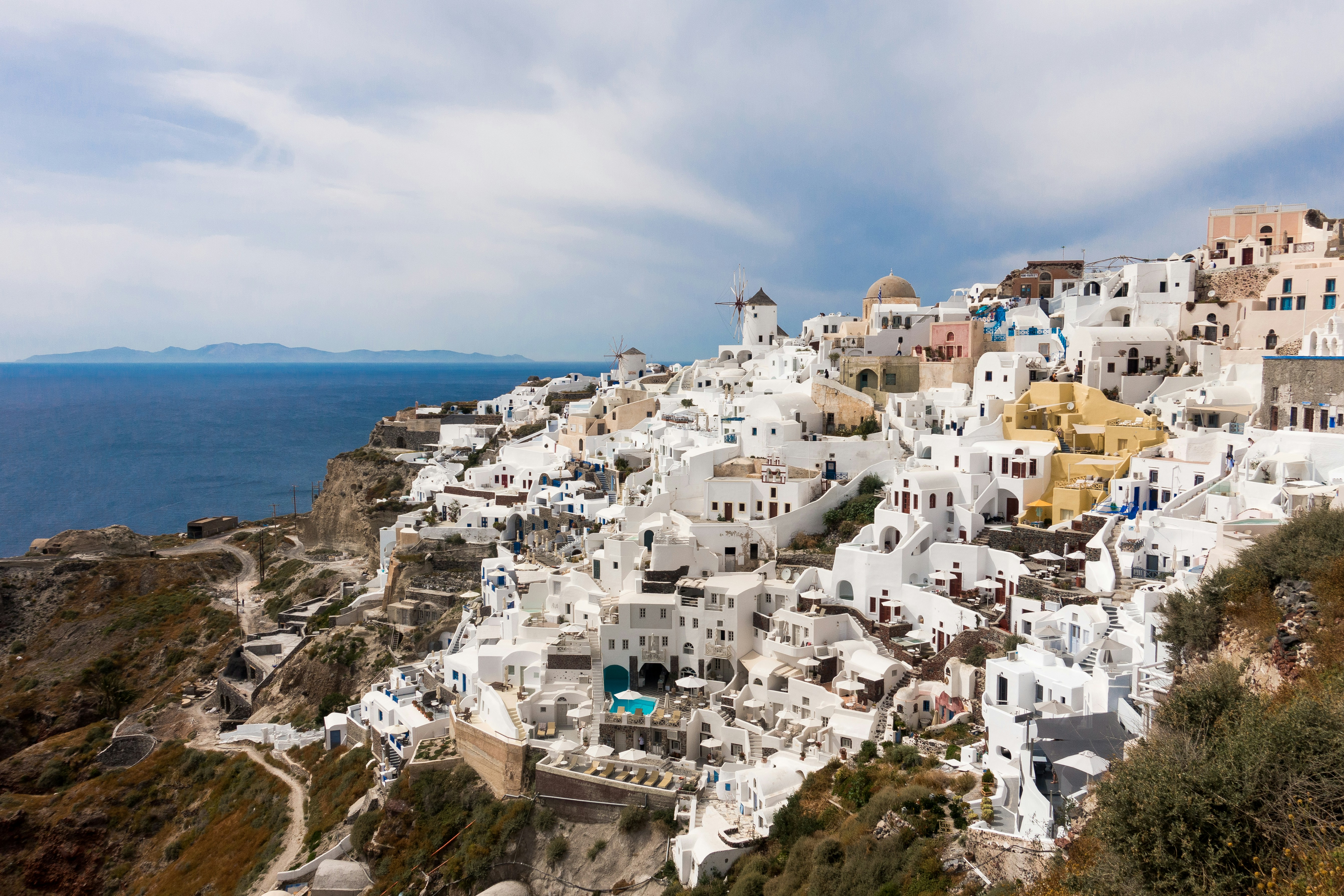 Cliffside village of whitewashed buildings overlooking the Aegean Sea under a partly cloudy sky.