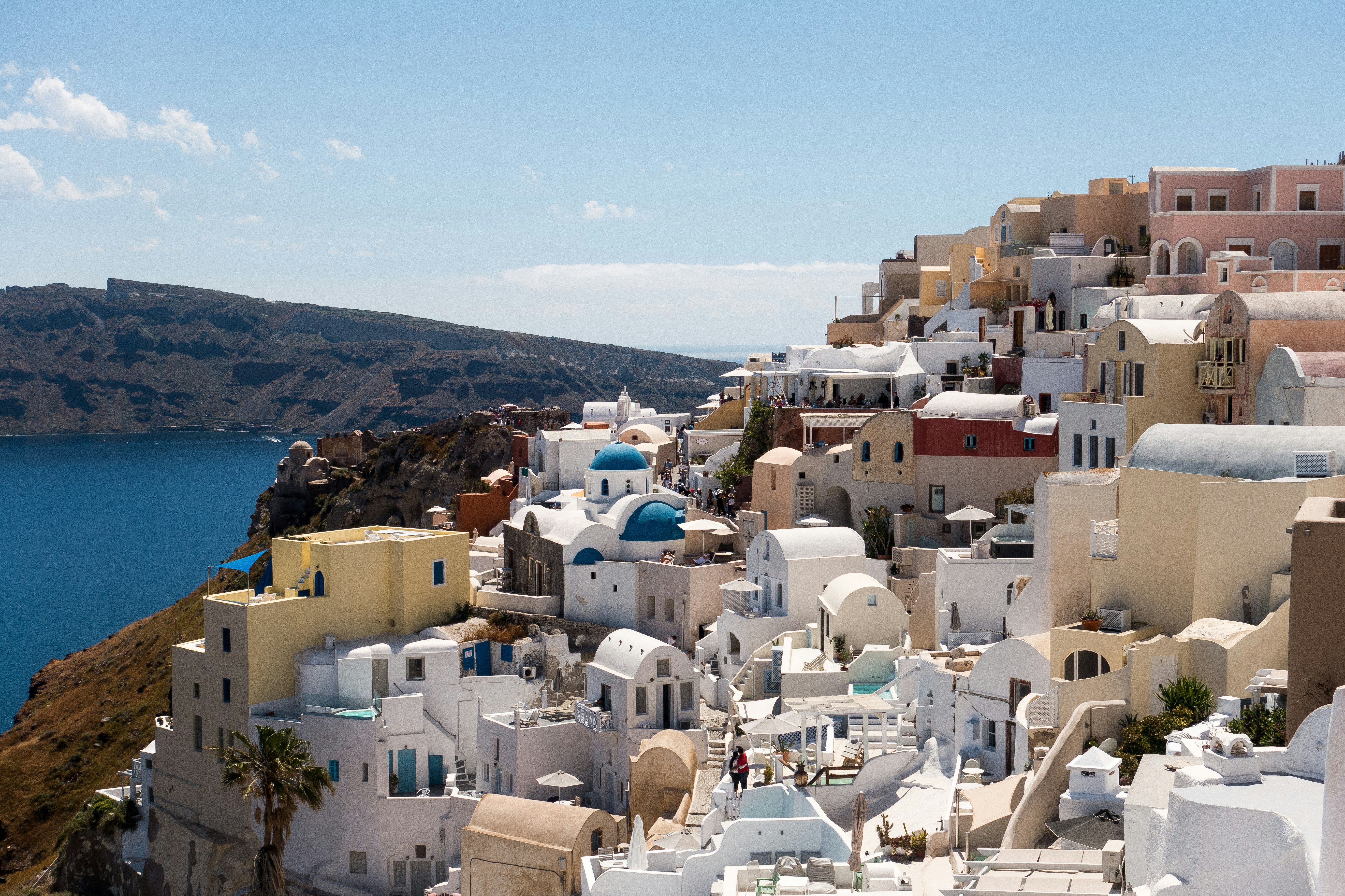 Whitewashed buildings with blue domes cascading down a cliffside overlooking the Aegean Sea.