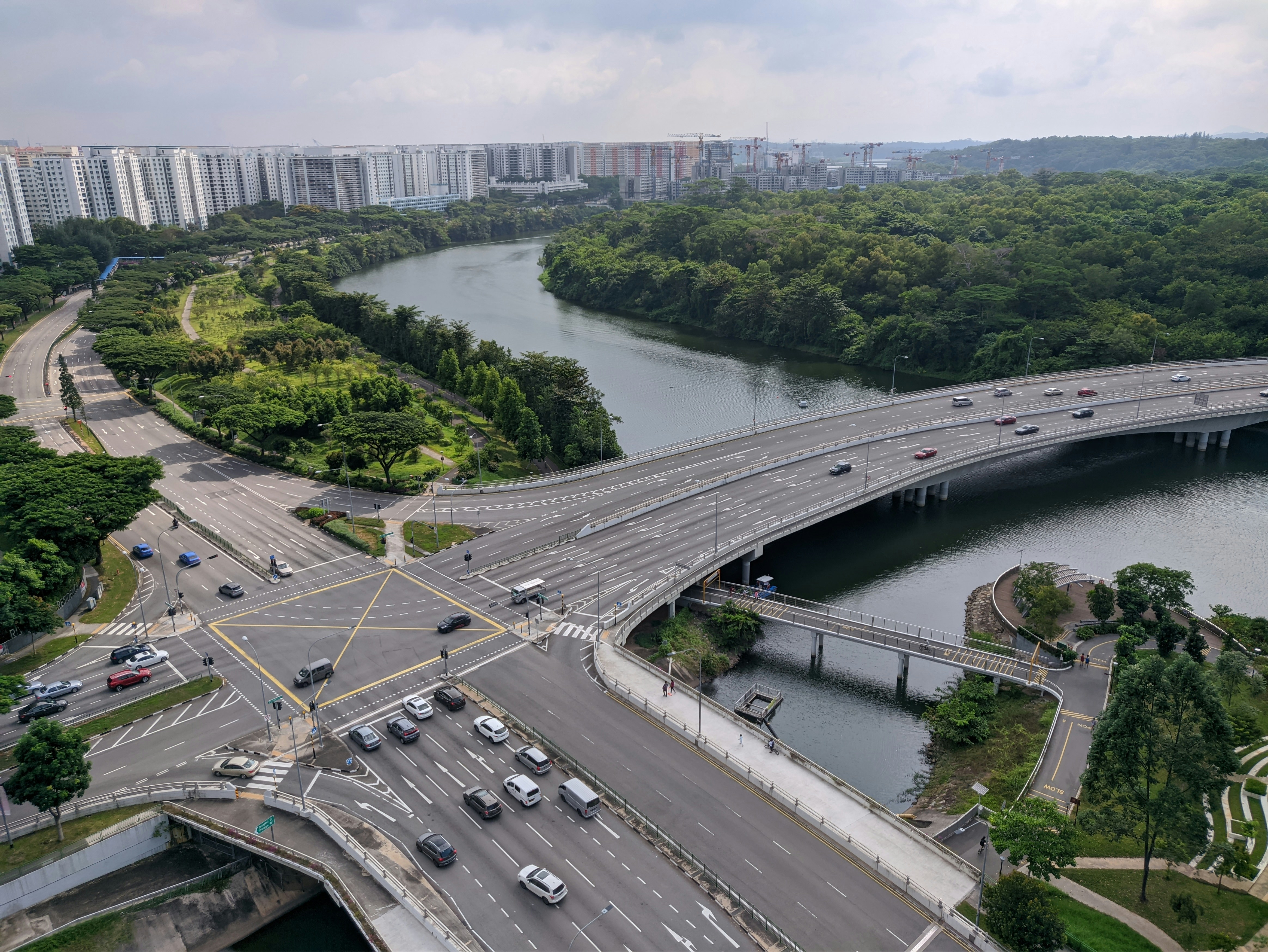 Aerial view showcasing the intersection of roadways and a winding river, surrounded by lush greenery and urban development.