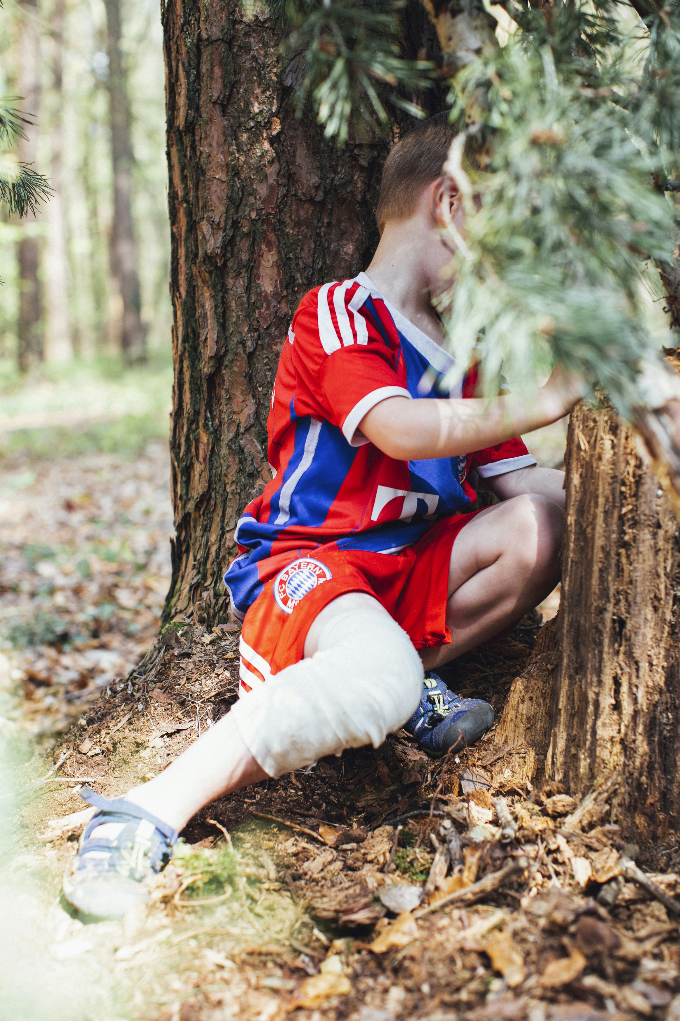 Child in Red Sportswear Hidden Behind a Tree in a Sunlit Forest