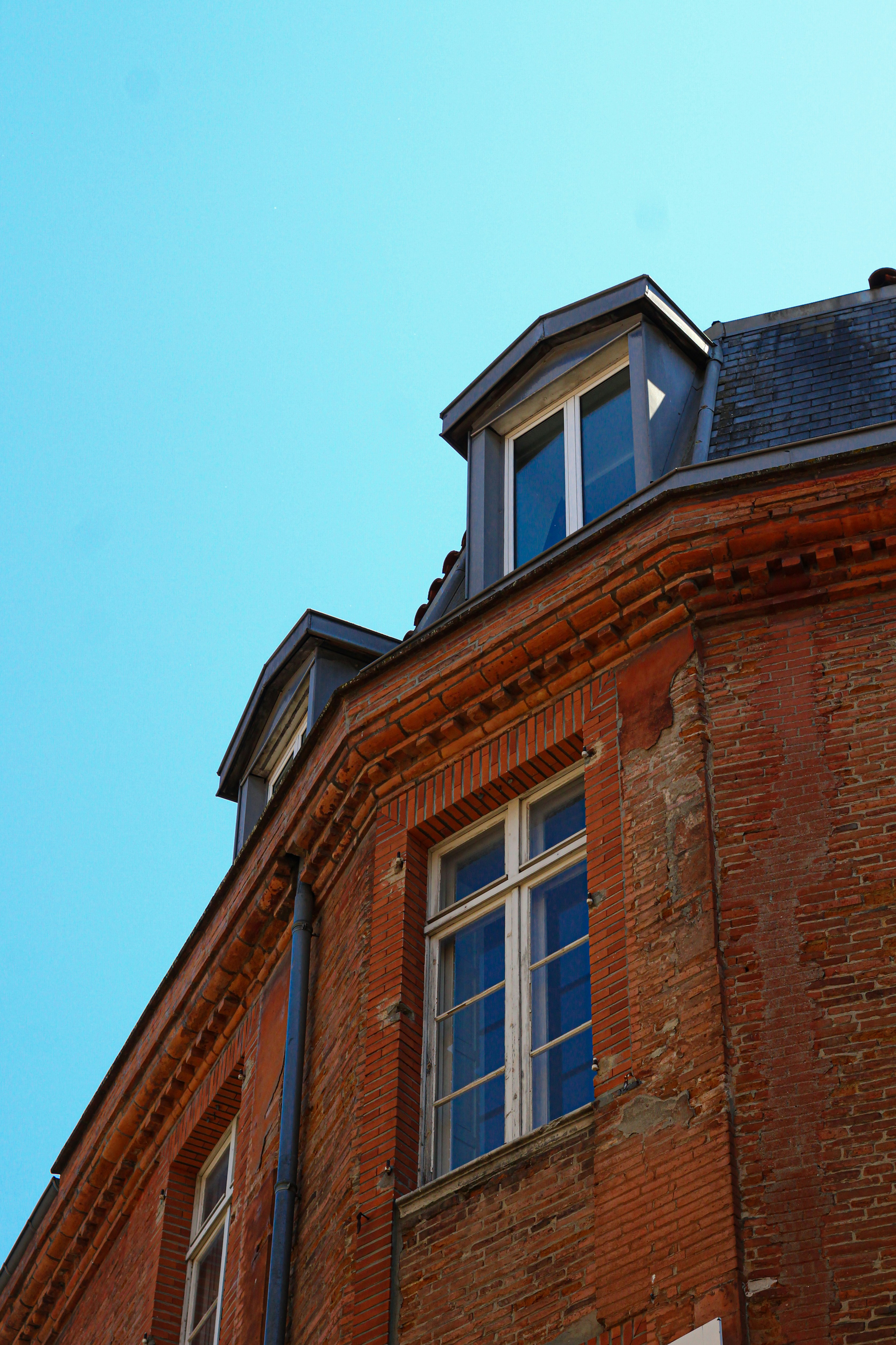 Brick building corner showcasing vintage architecture with modern windows under a clear blue sky.