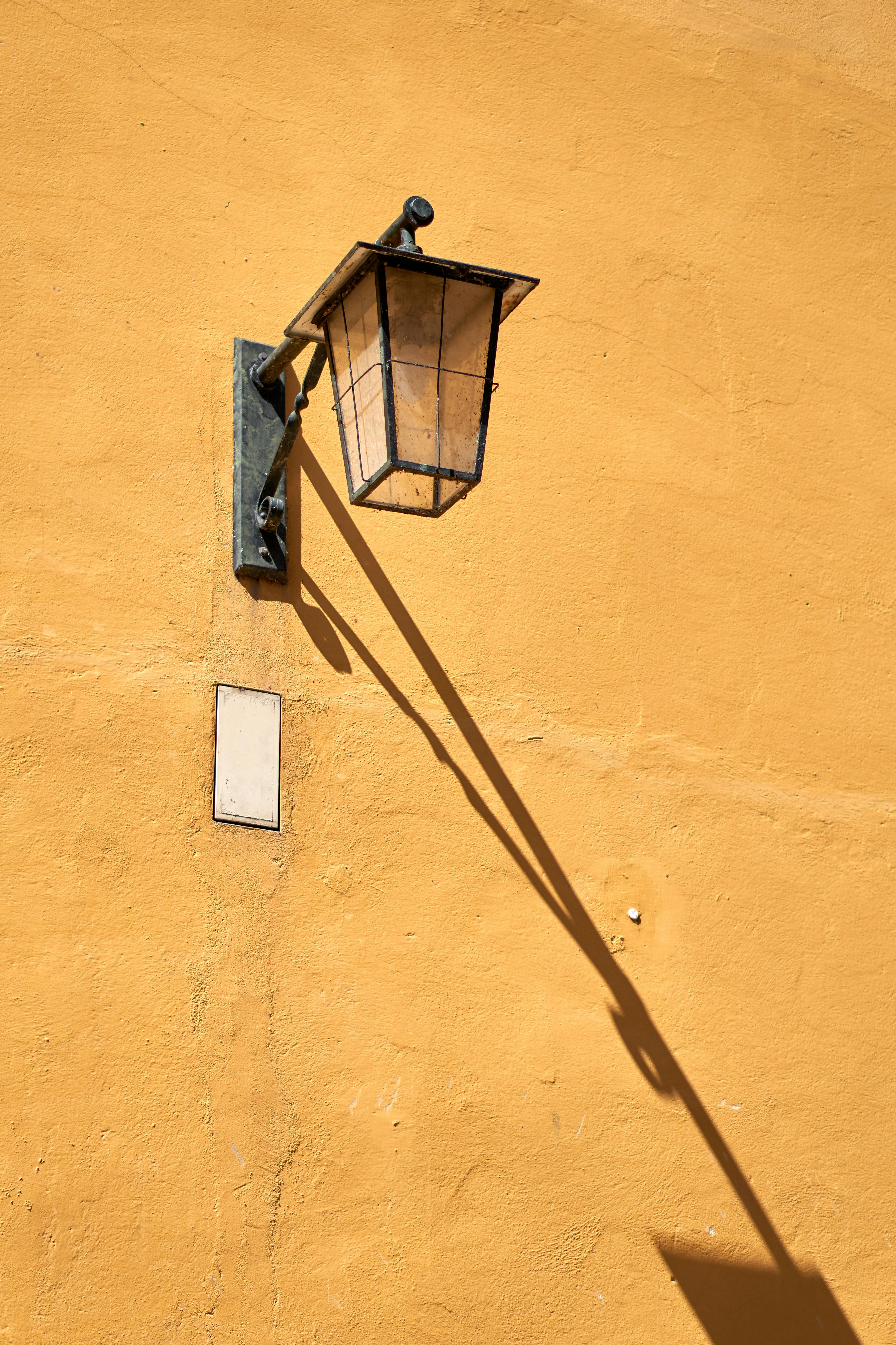 Streetlamp casting a long shadow on a textured yellow wall.