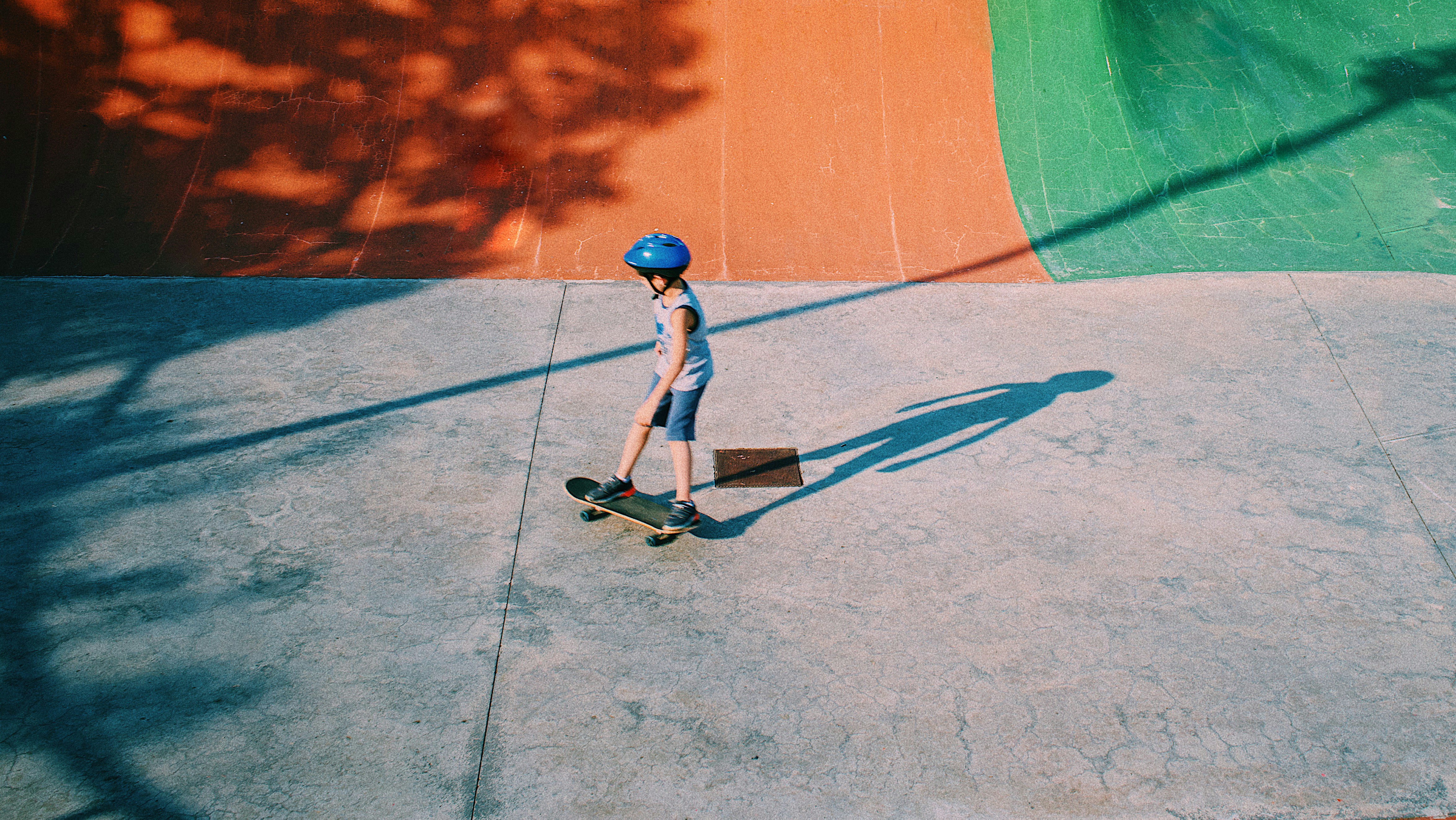 Child in blue helmet skateboarding on a colorful ramp under dappled sunlight.
