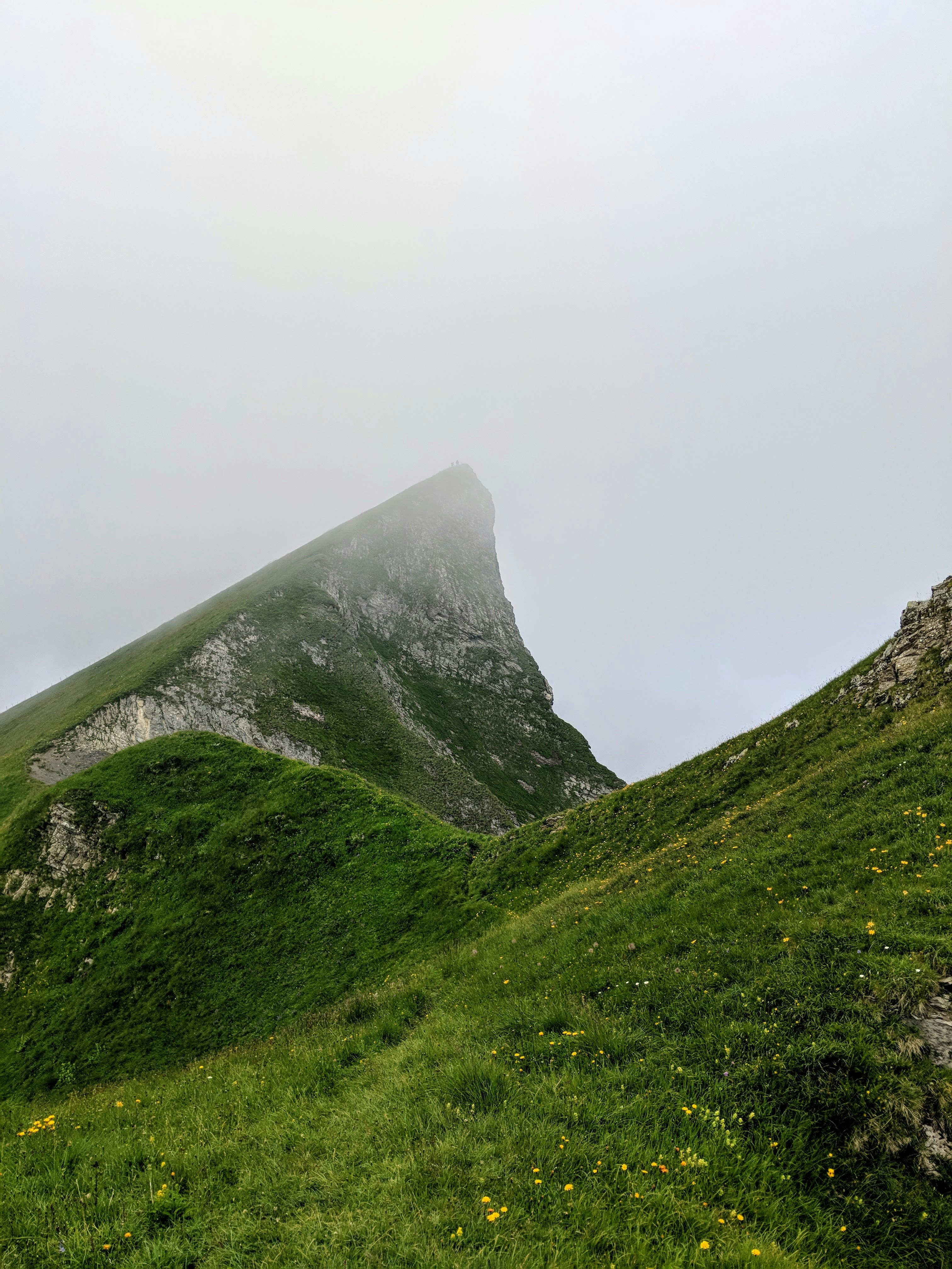 A mist-shrouded mountain peak rises above lush green hills, hinting at the grandeur hidden within the clouds.