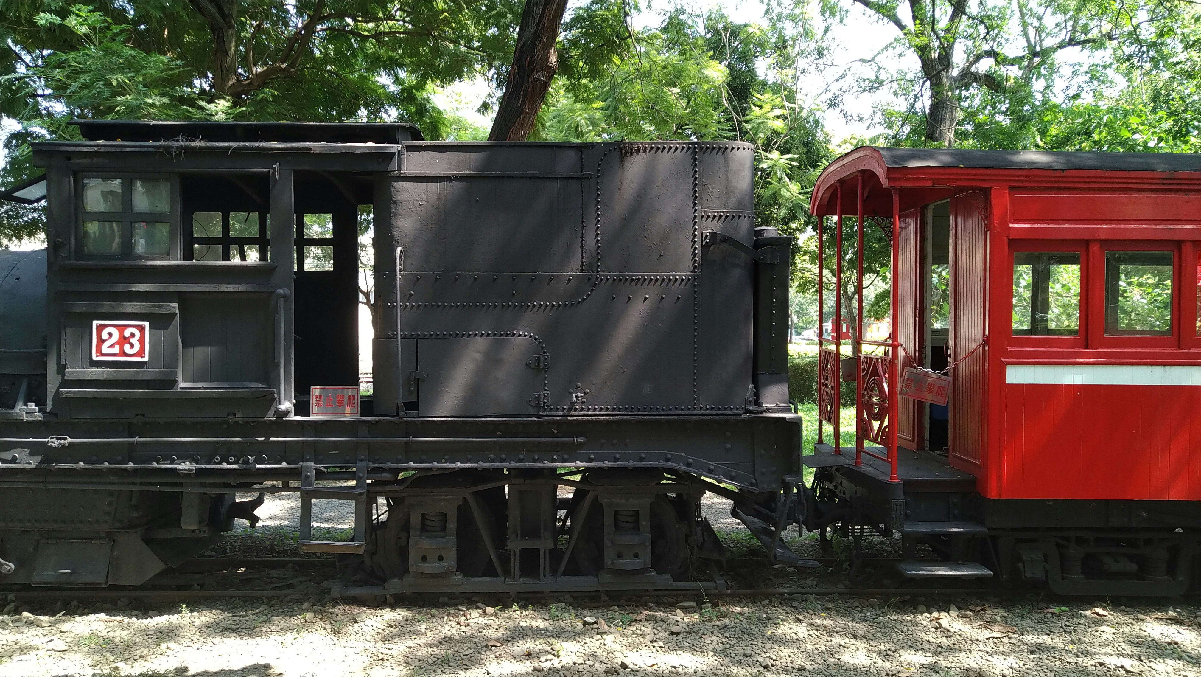 Historic black locomotive and vibrant red passenger car side by side in a lush setting.