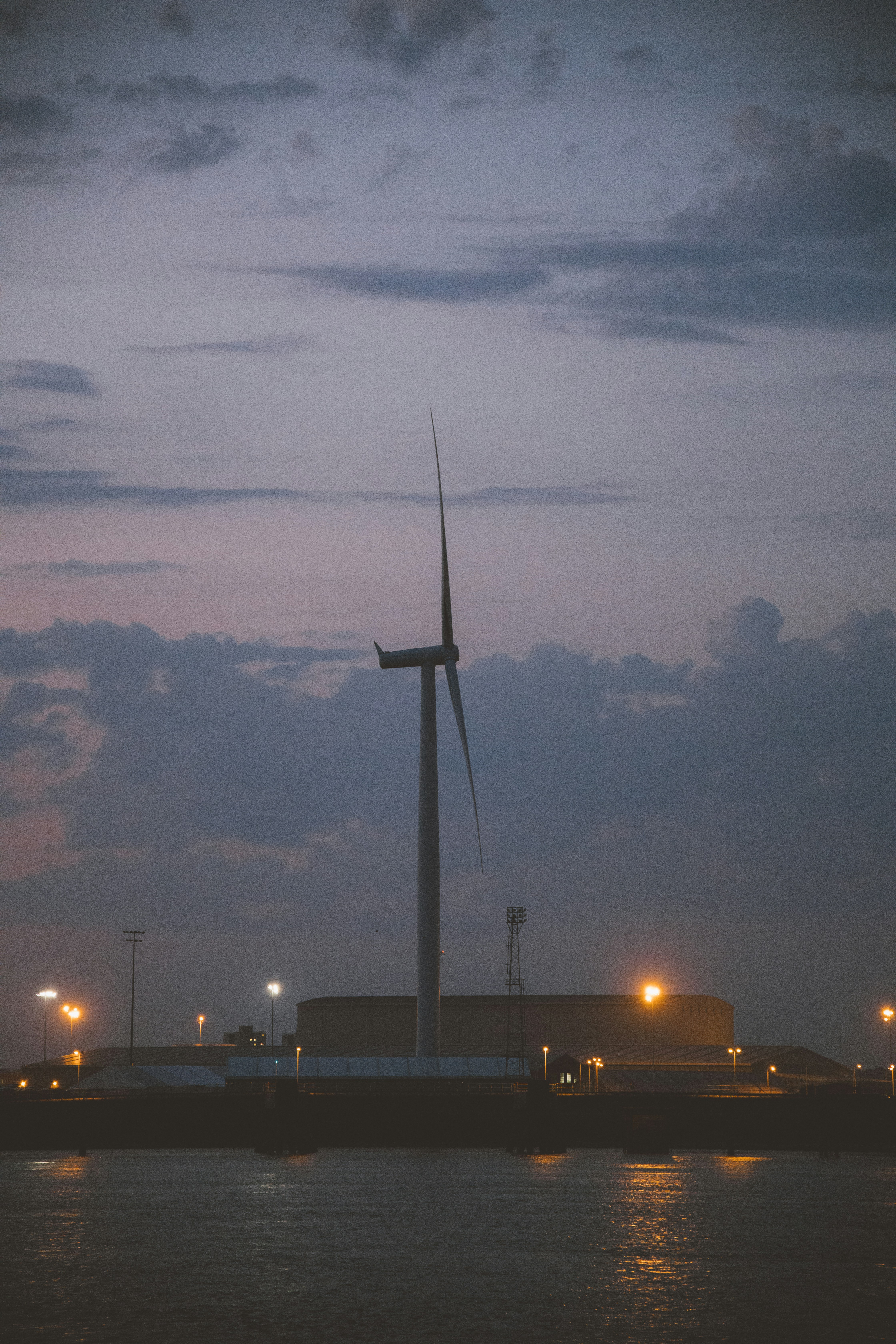 Blue-hour turbine over a quiet harbor under pastel skies
