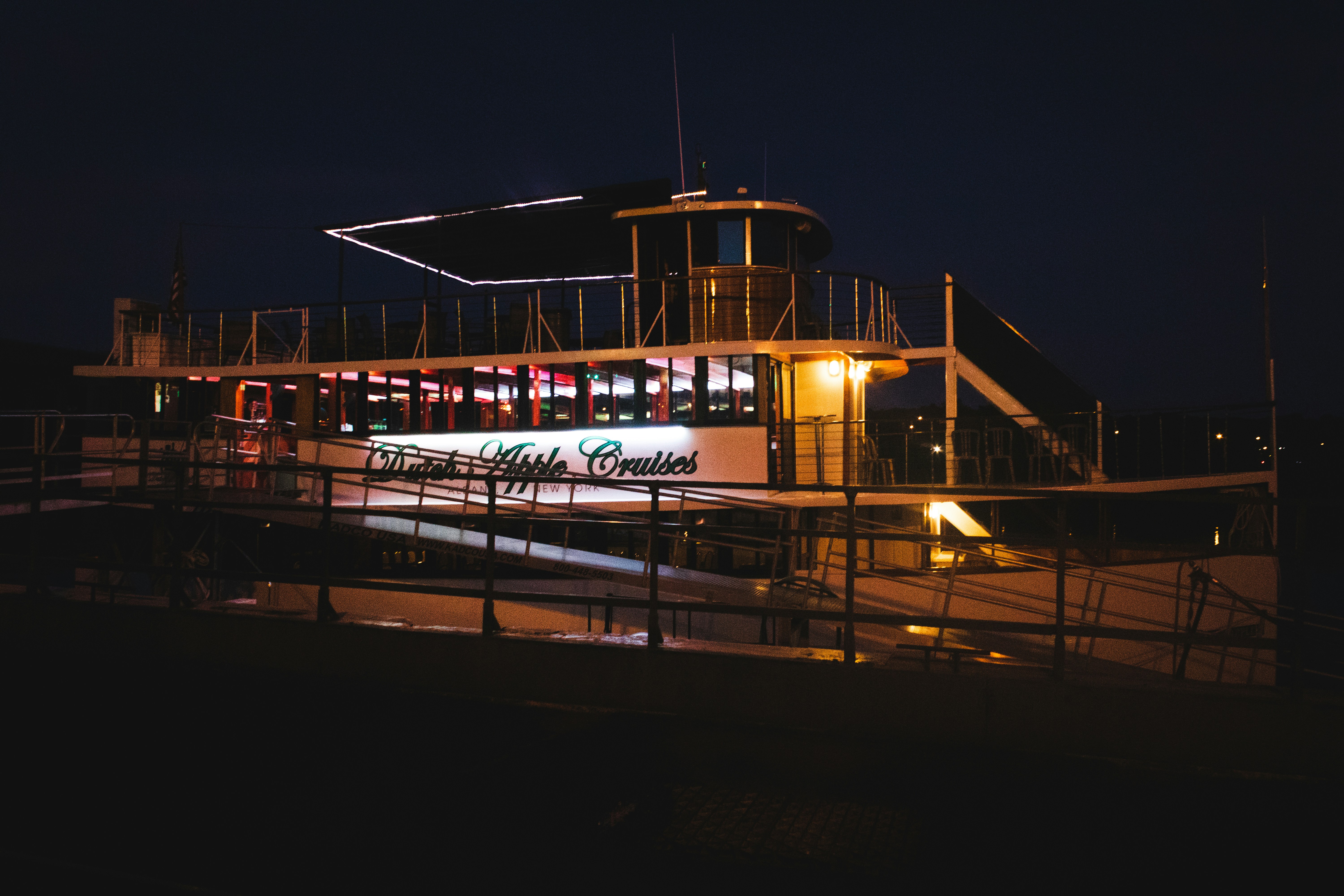 A beautifully lit cruise boat docked at night, showcasing its illuminated signage against the dark backdrop of the water. The structure's modern design contrasts with the serene environment.