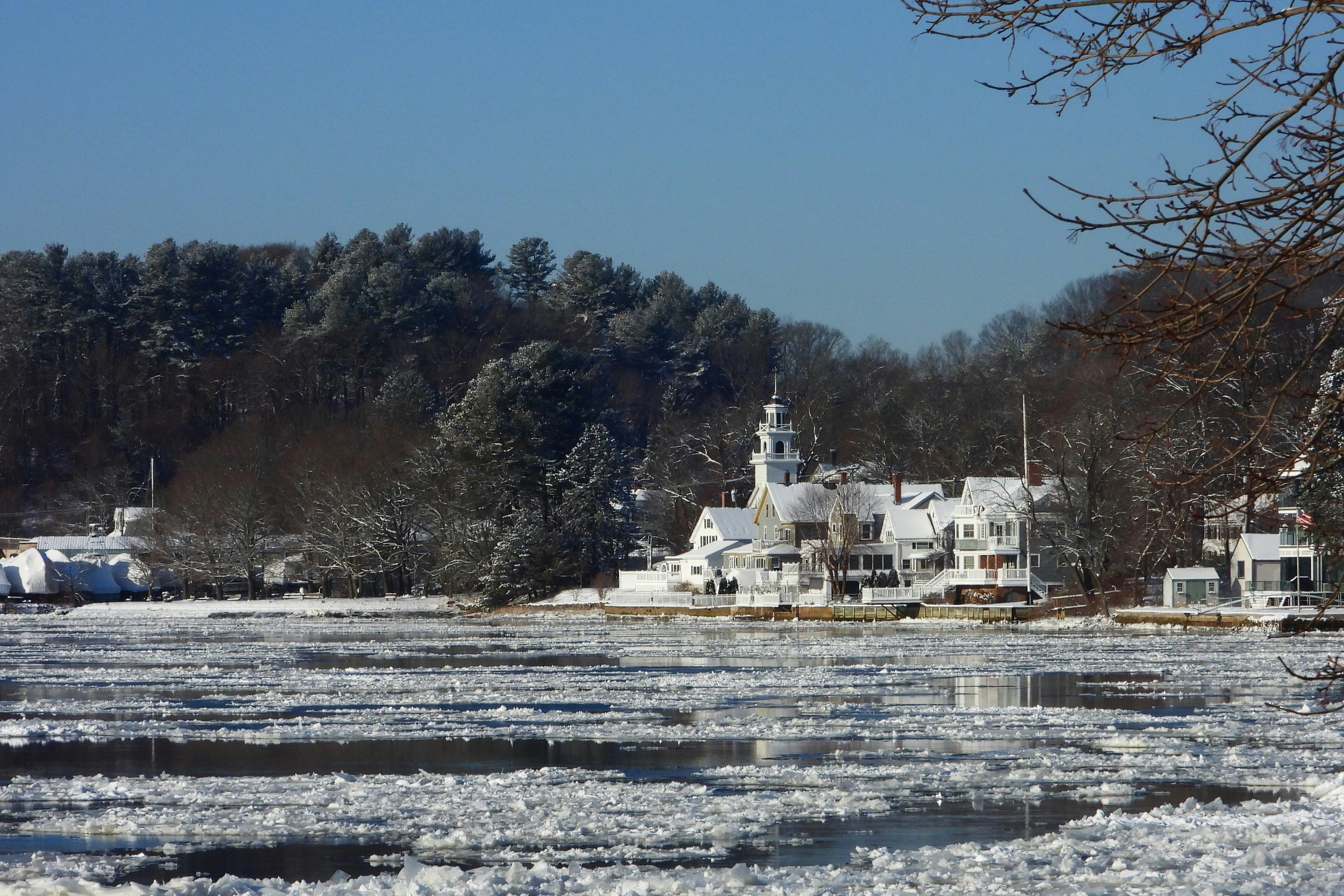 Snow-covered village by a frozen river under clear blue skies.