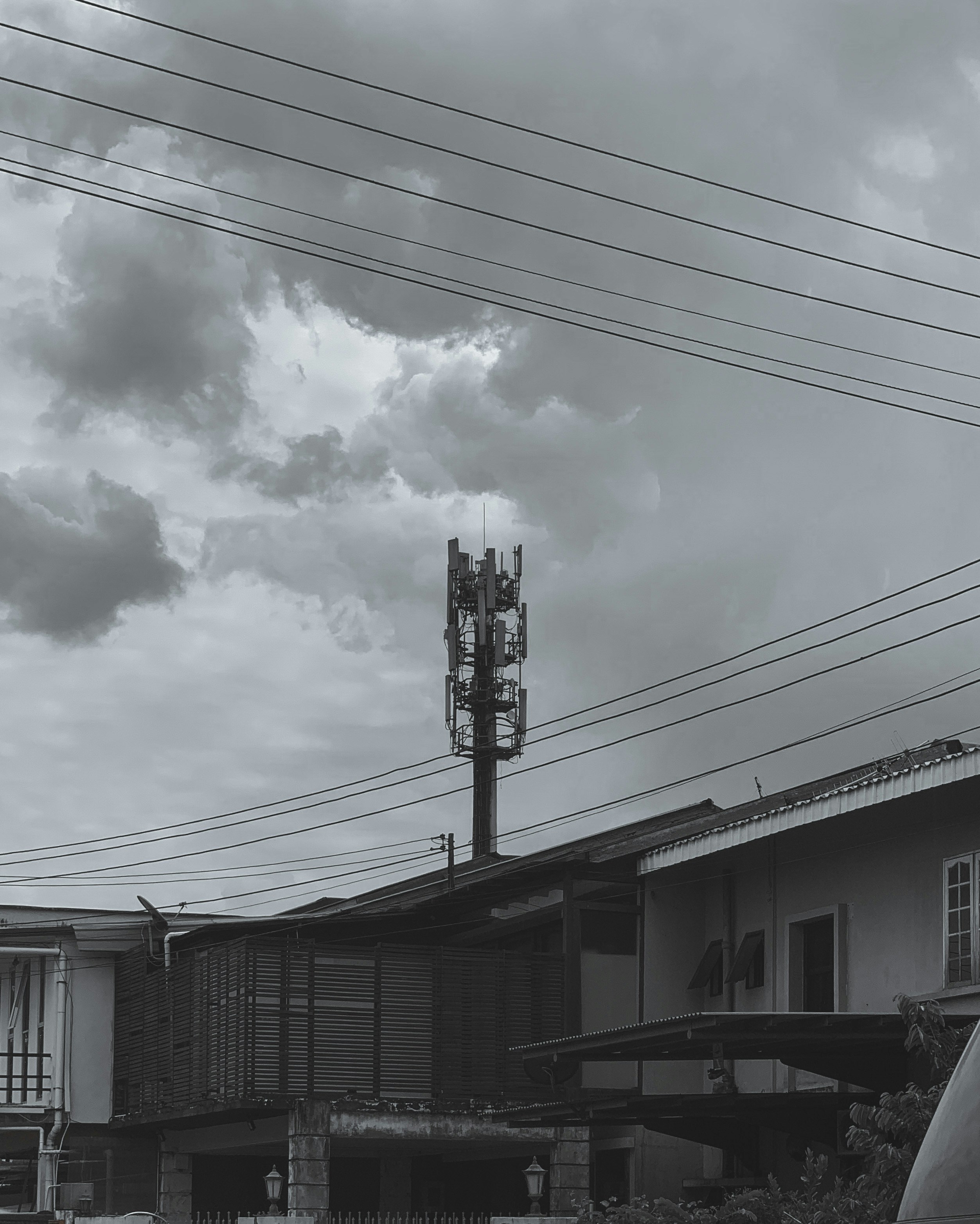 Cell tower rising above urban structures under a dramatic sky, showcasing the blend of technology and architecture.