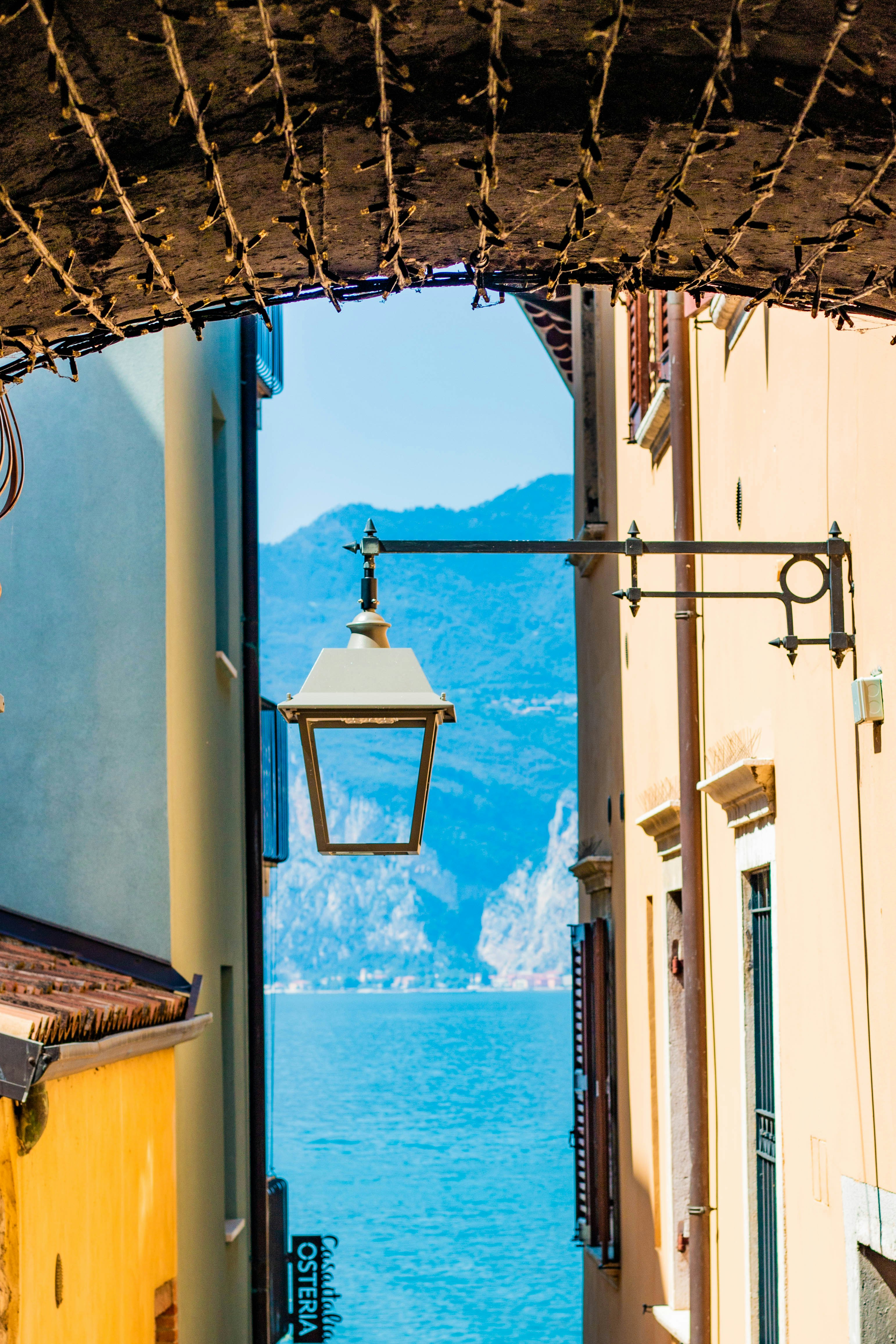 Charming alleyway framed by colorful buildings leading to serene lake views, with a vintage lantern enhancing the ambiance.