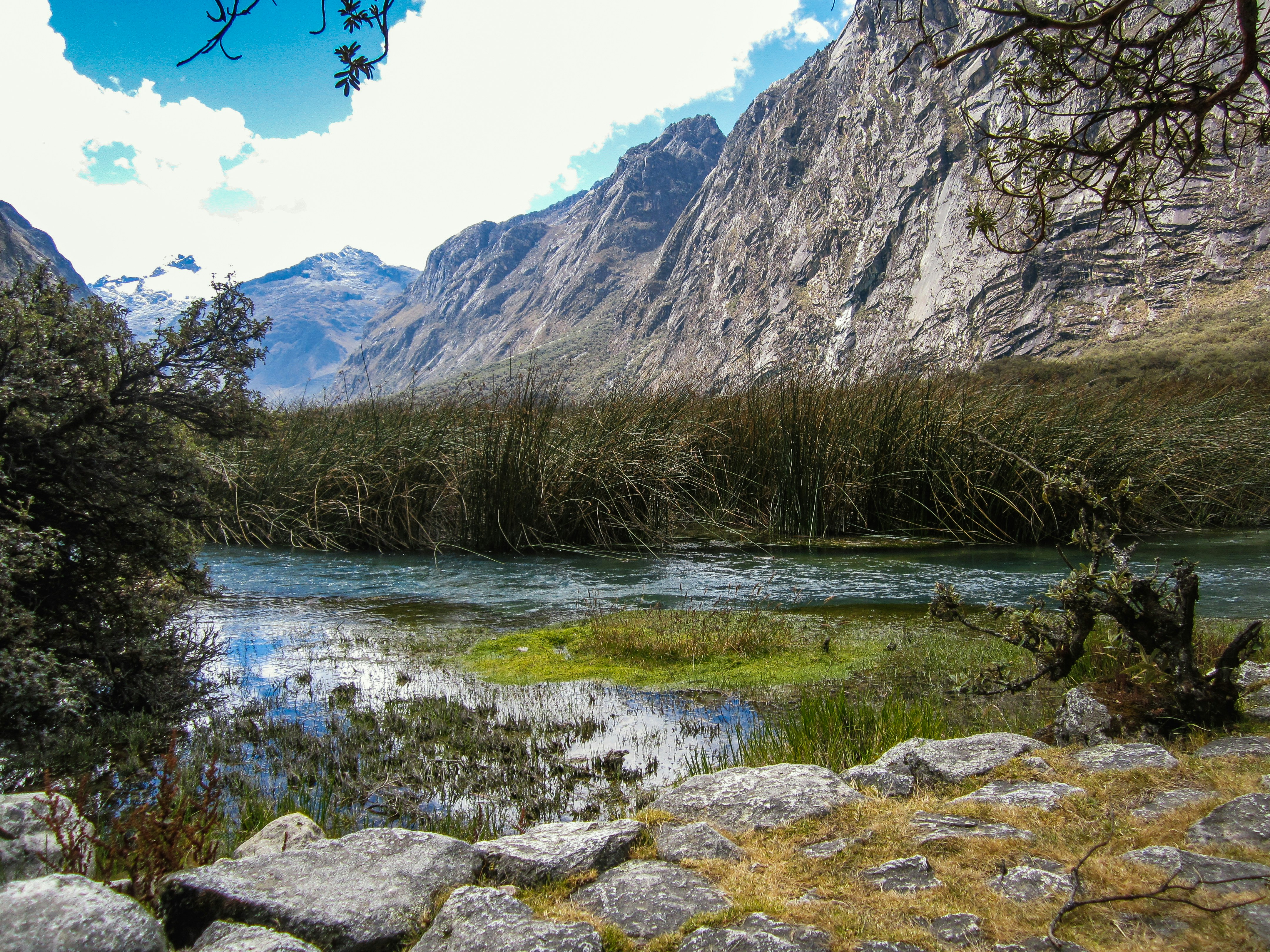 Mountain valley with a calm river flowing through, surrounded by rugged cliffs and clear blue sky.