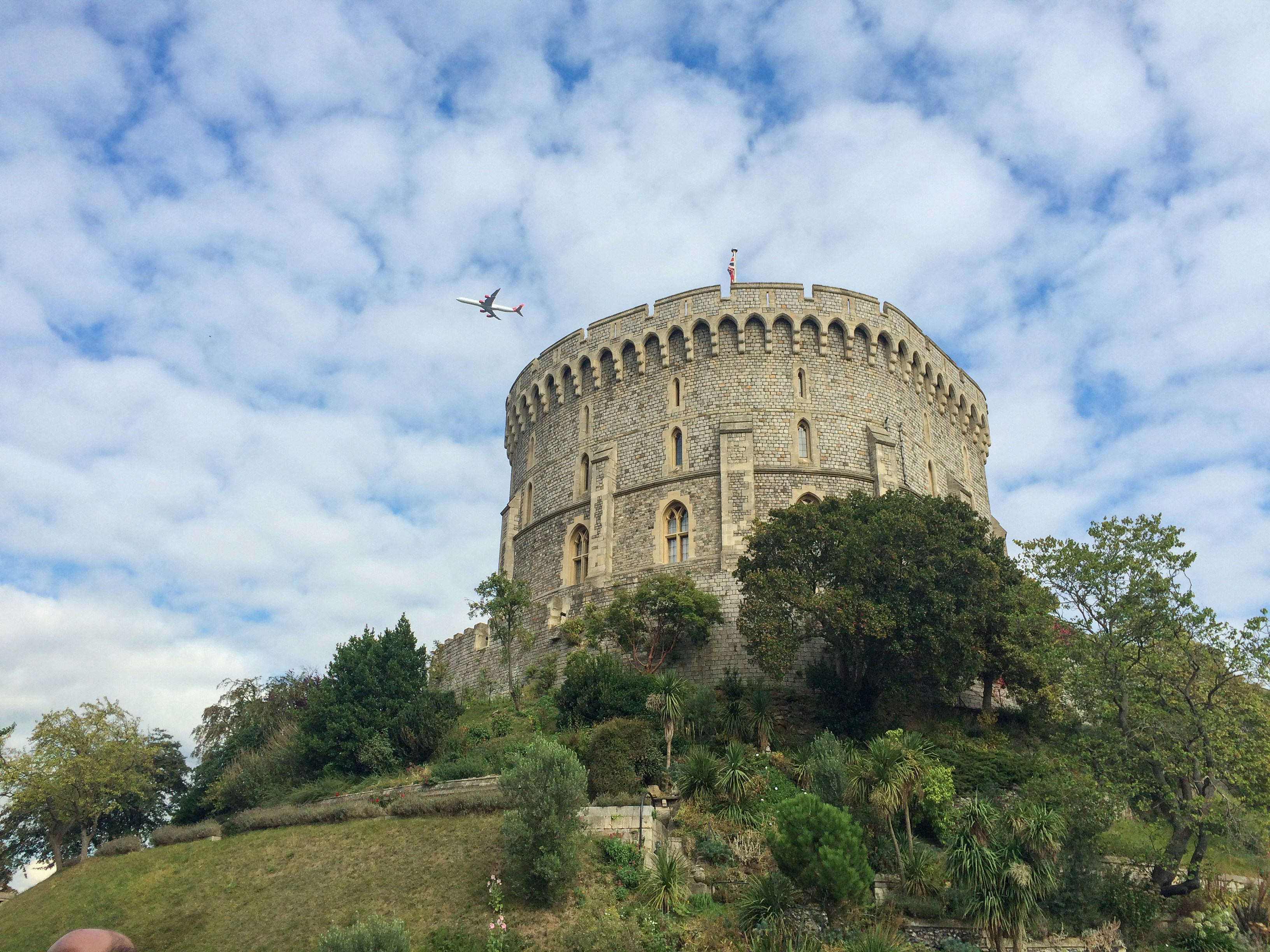 Circular stone tower atop a hill surrounded by lush greenery under a sky filled with scattered clouds.