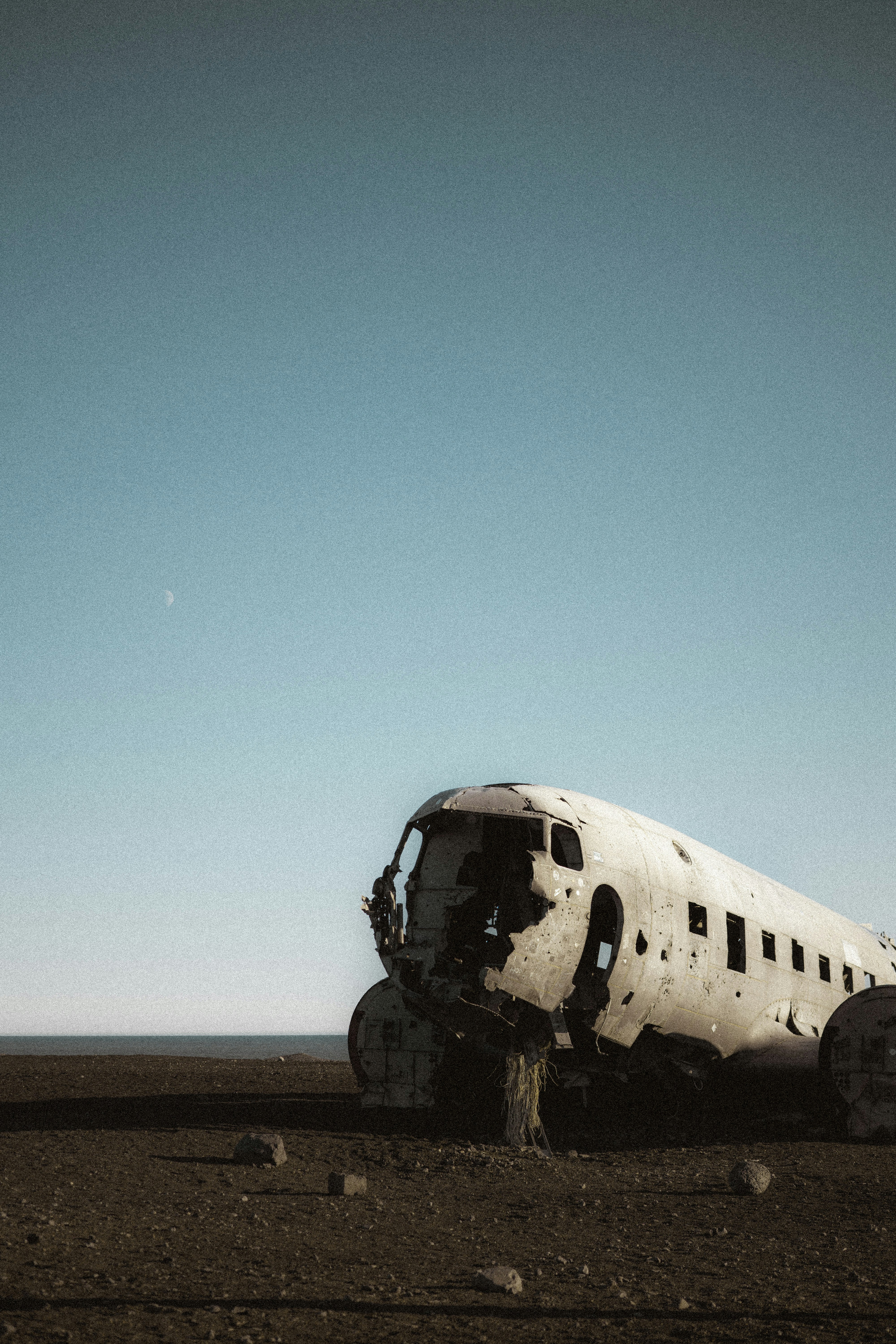 Abandoned aircraft fuselage rests on a barren landscape under a clear blue sky, evoking a sense of nostalgia and desolation.