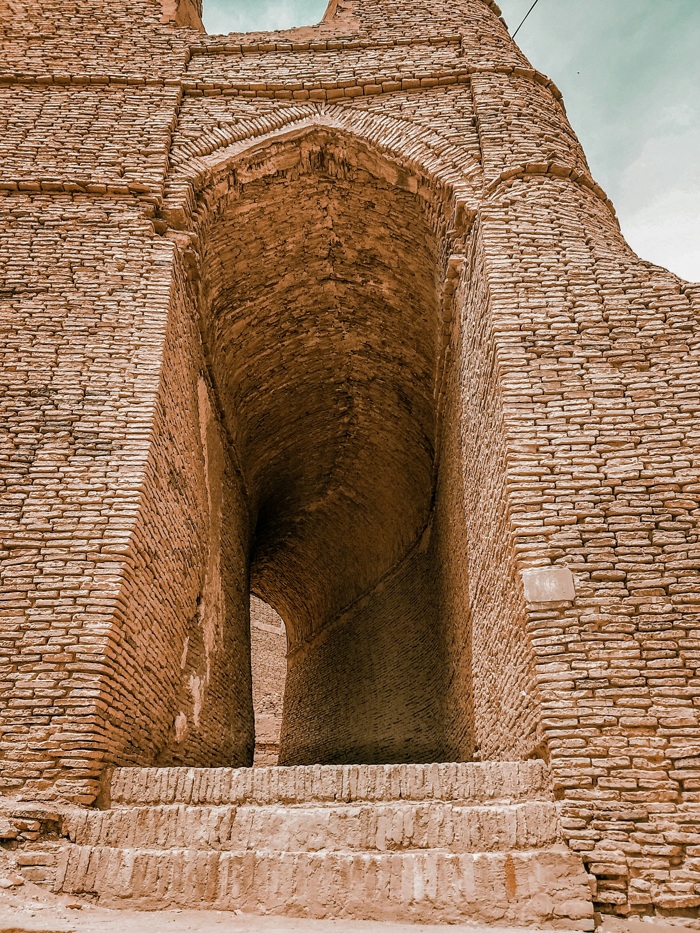 Arched entrance of a historic brick structure, showcasing intricate textures and a sense of depth. The scene invites exploration into the past.