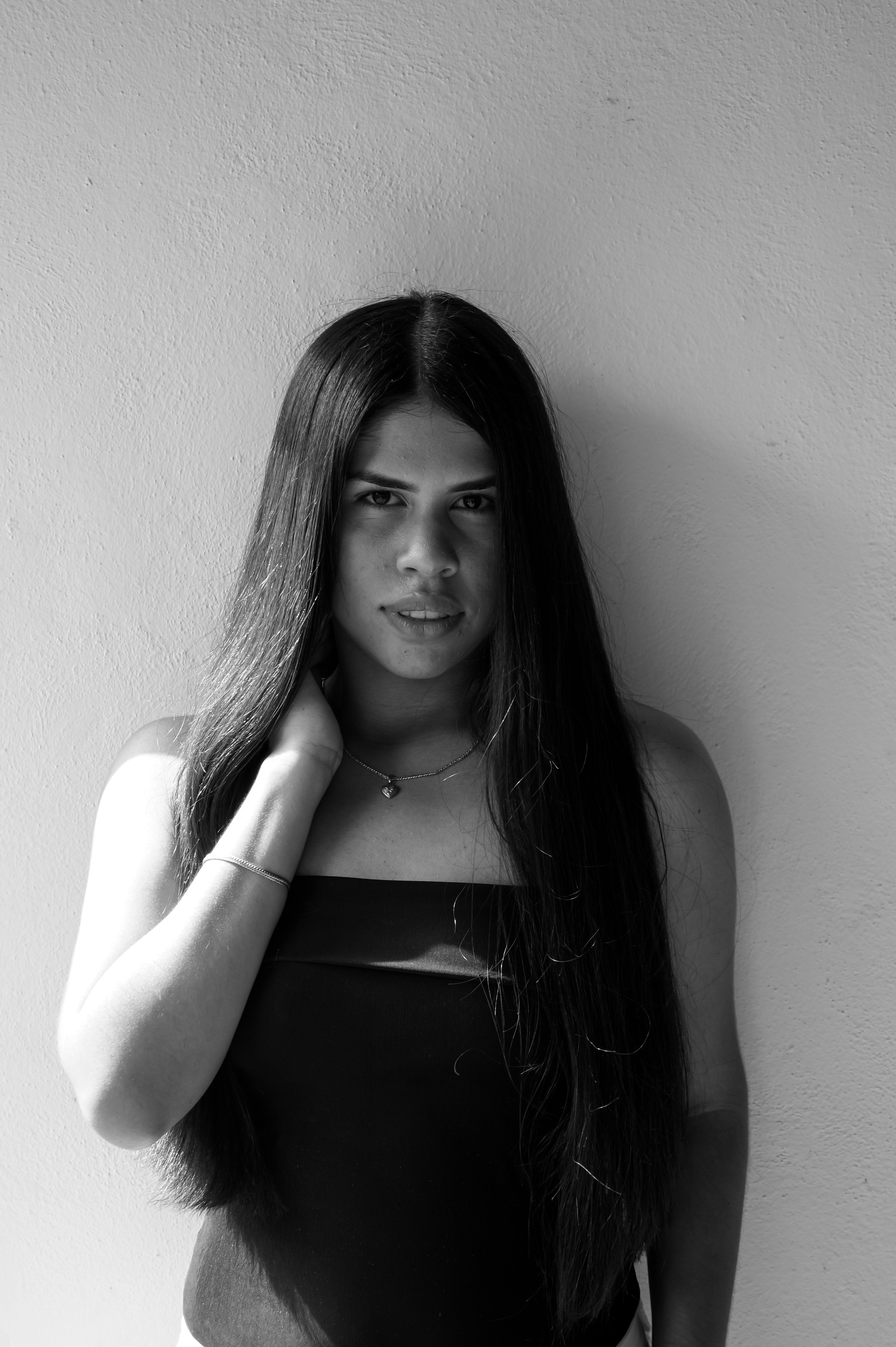 Woman with long hair poses against a textured wall in soft lighting.