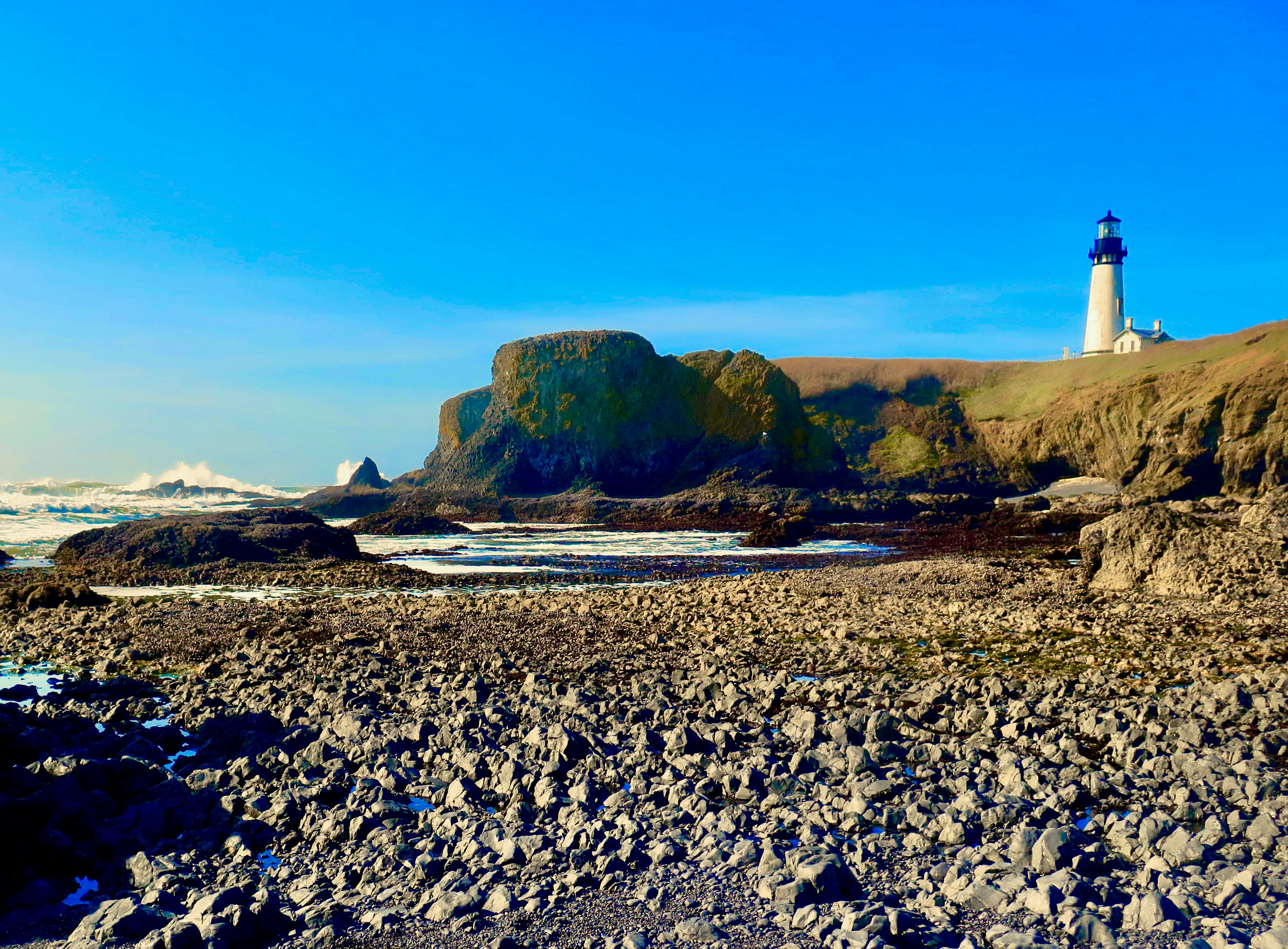 Rocky shoreline leading to a distant lighthouse under a vivid blue sky.