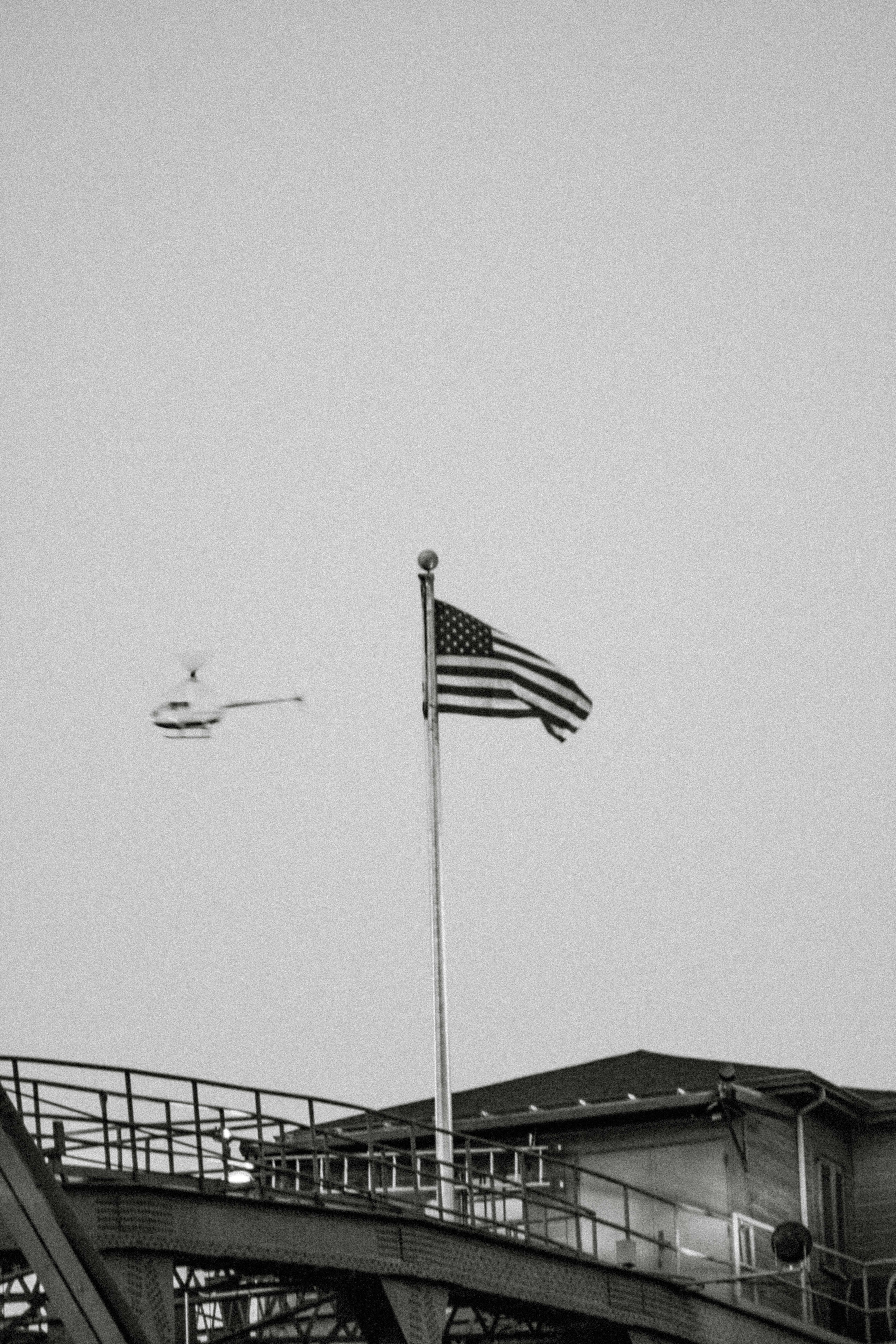 American flag waving gently beside a helicopter in flight against a muted sky.