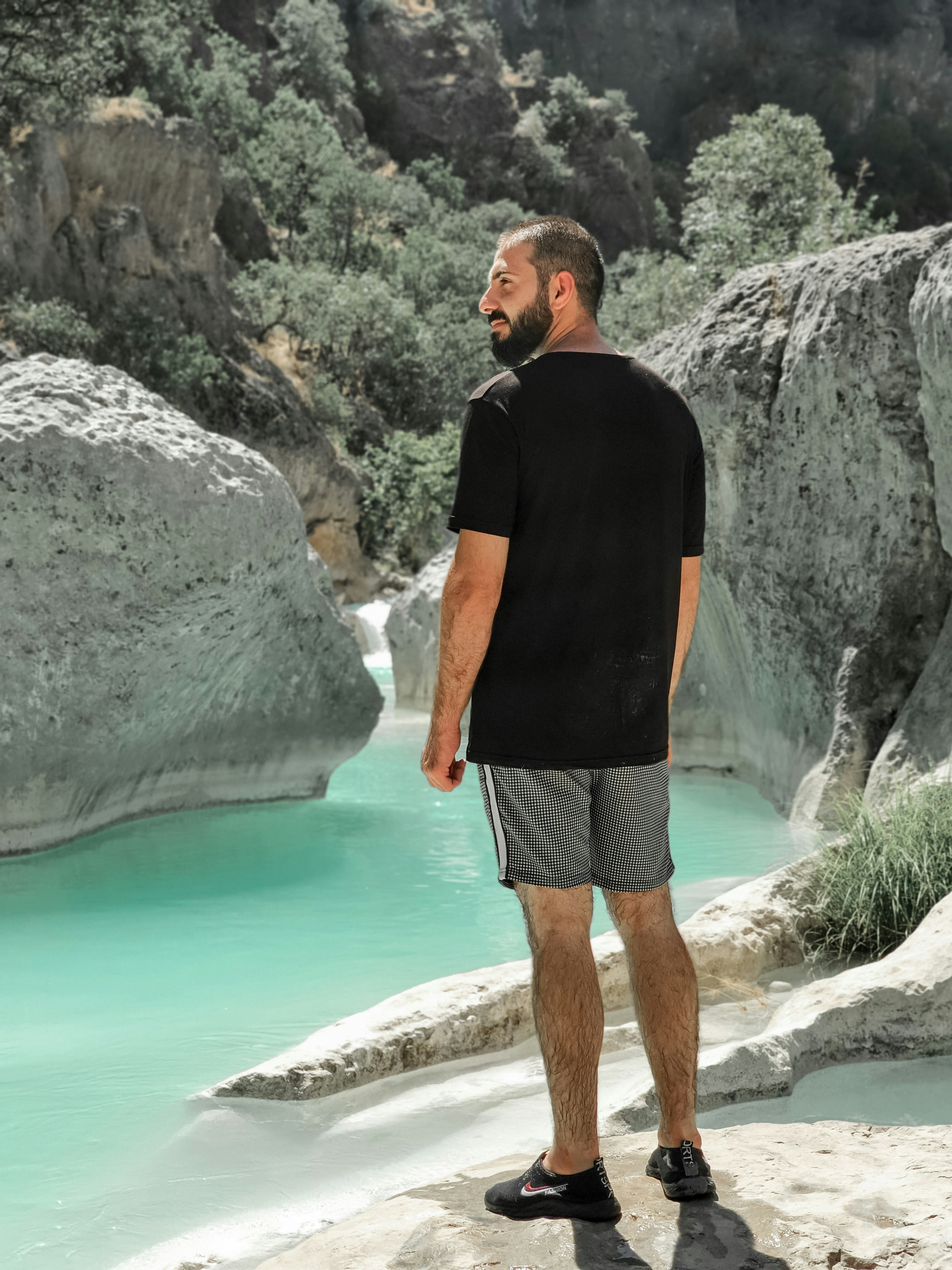 man in black t-shirt standing on rock near body of water during daytime