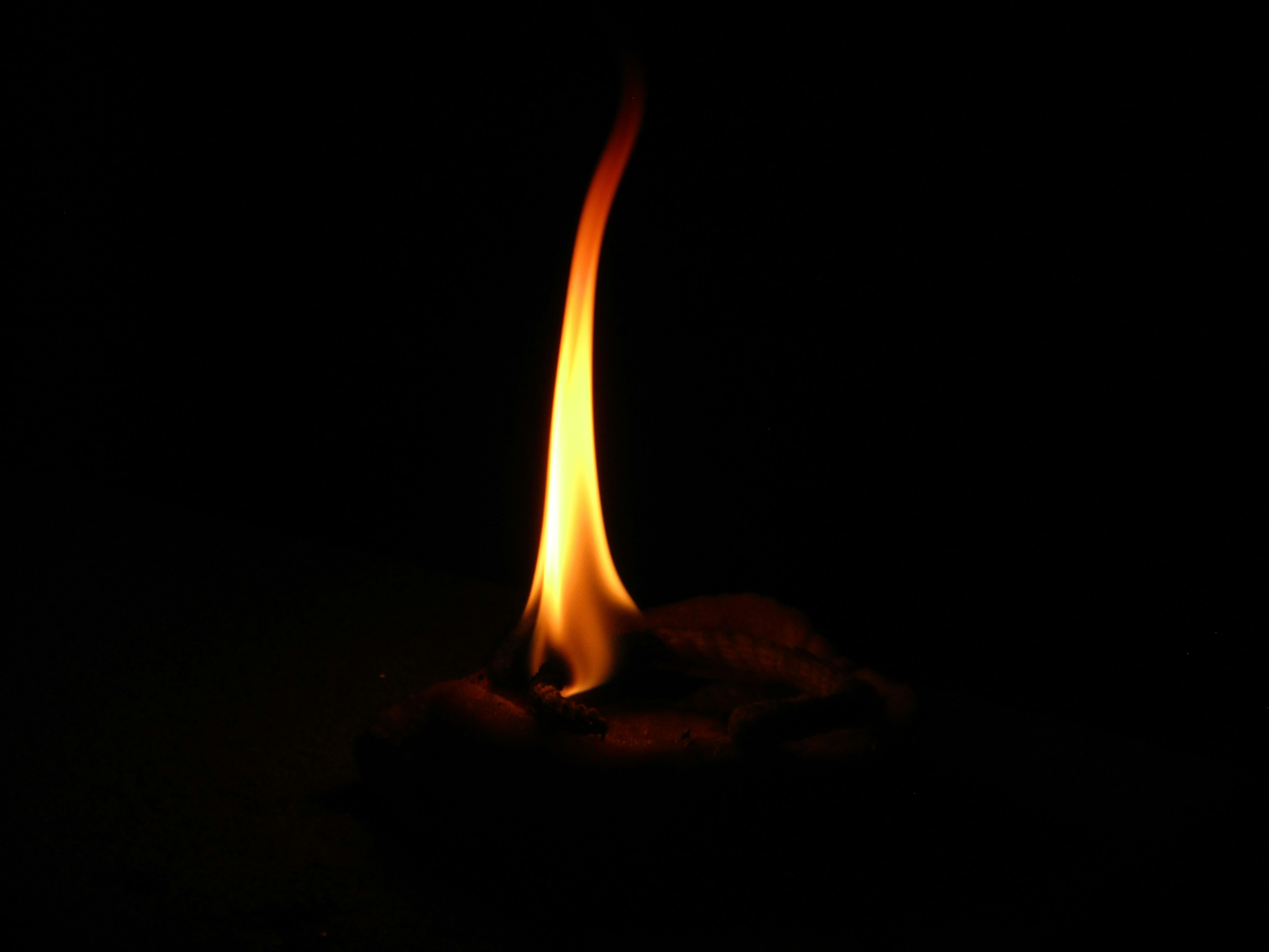 A vibrant flame flickers above a small source, casting soft light in a dark environment. The contrast highlights the mesmerizing movement of the fire.