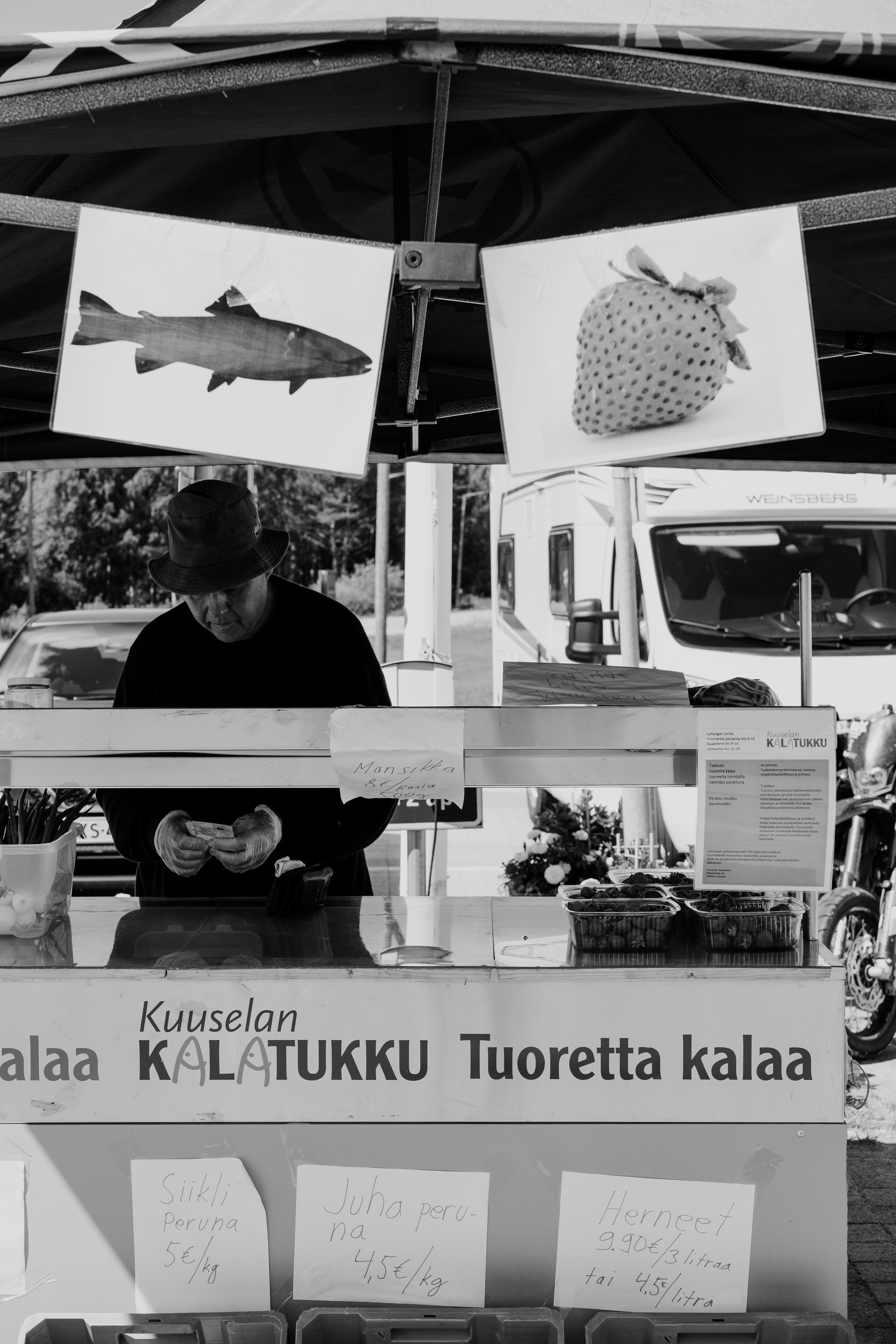 Monochrome Market: A Quiet Vendor Beneath Hanging Signs