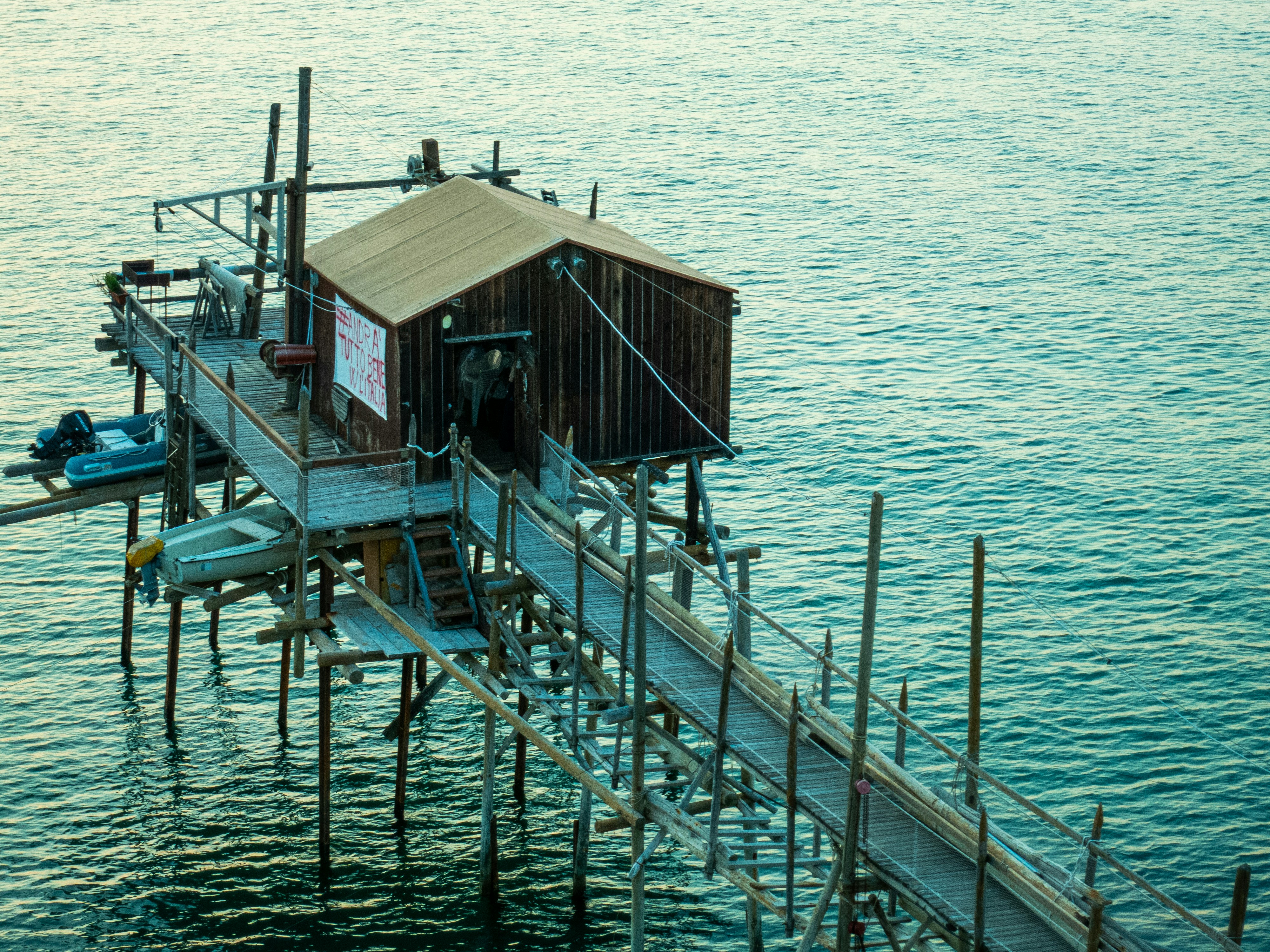 Wooden cabin perched on a dock over tranquil ocean waters during the day.