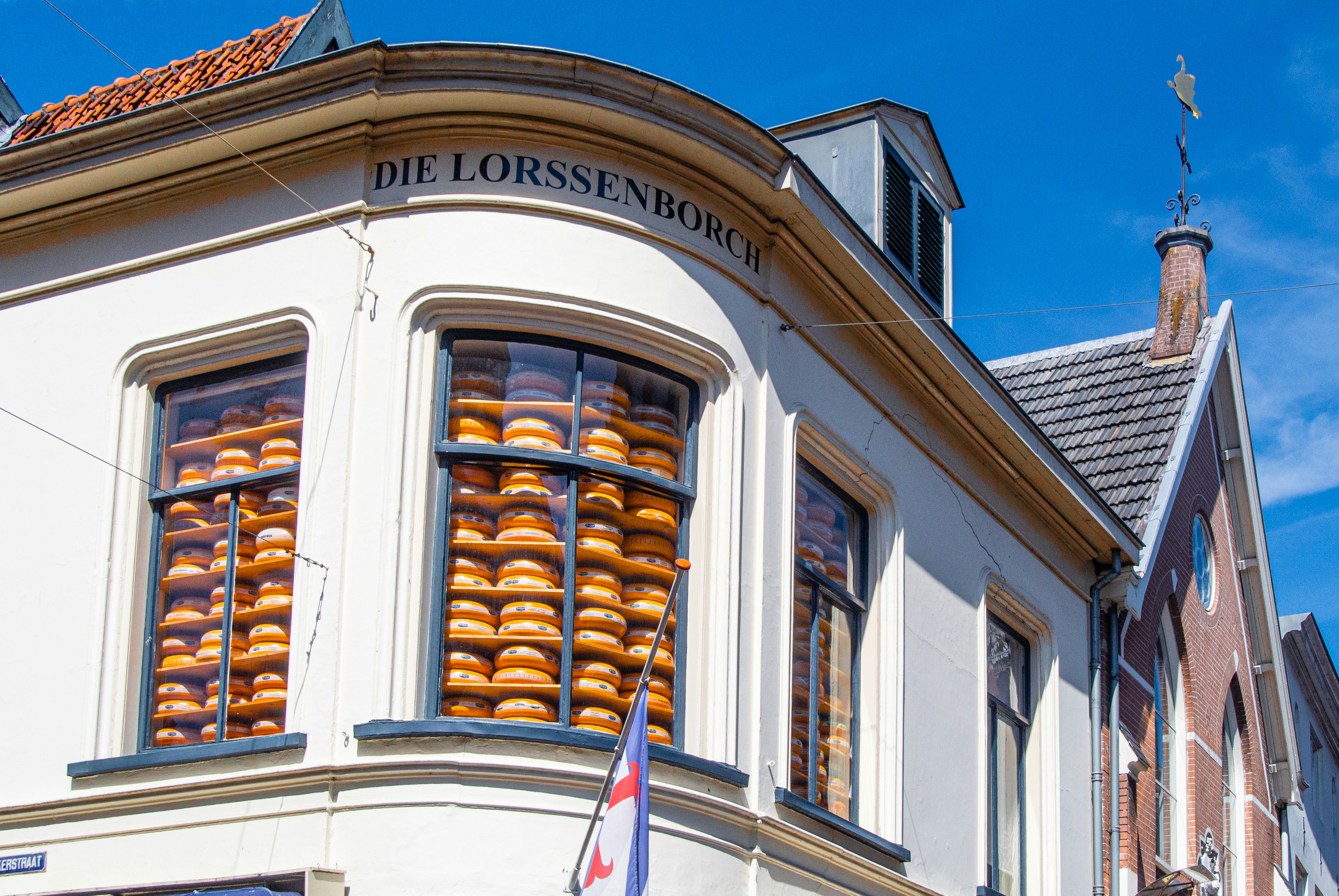 Rows of cheese wheels stacked in the windows of a historic building under a clear blue sky.