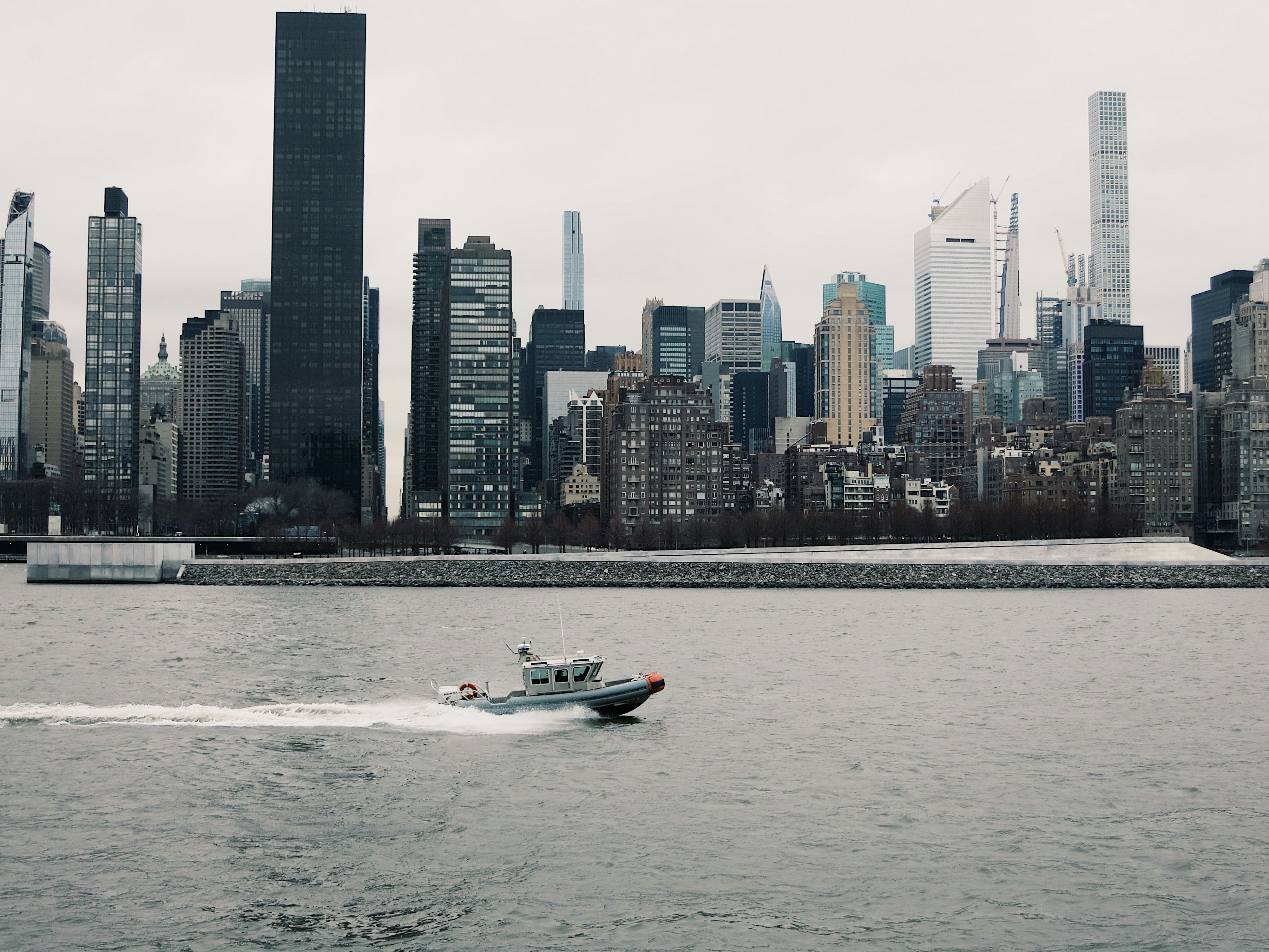 Speedboat cruising past a city skyline under overcast skies.