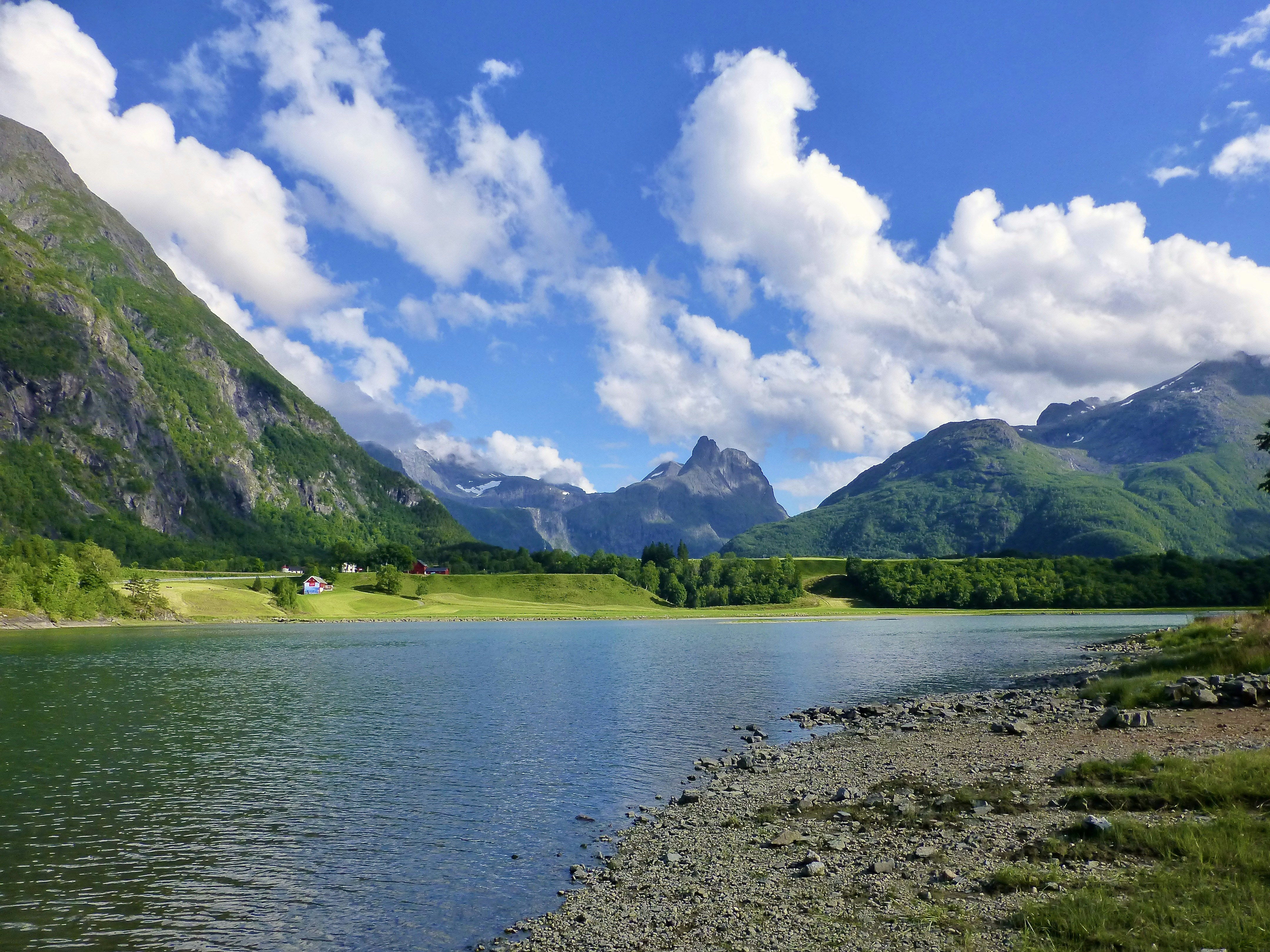 River flowing through lush green fjords under vibrant blue sky with clouds.
