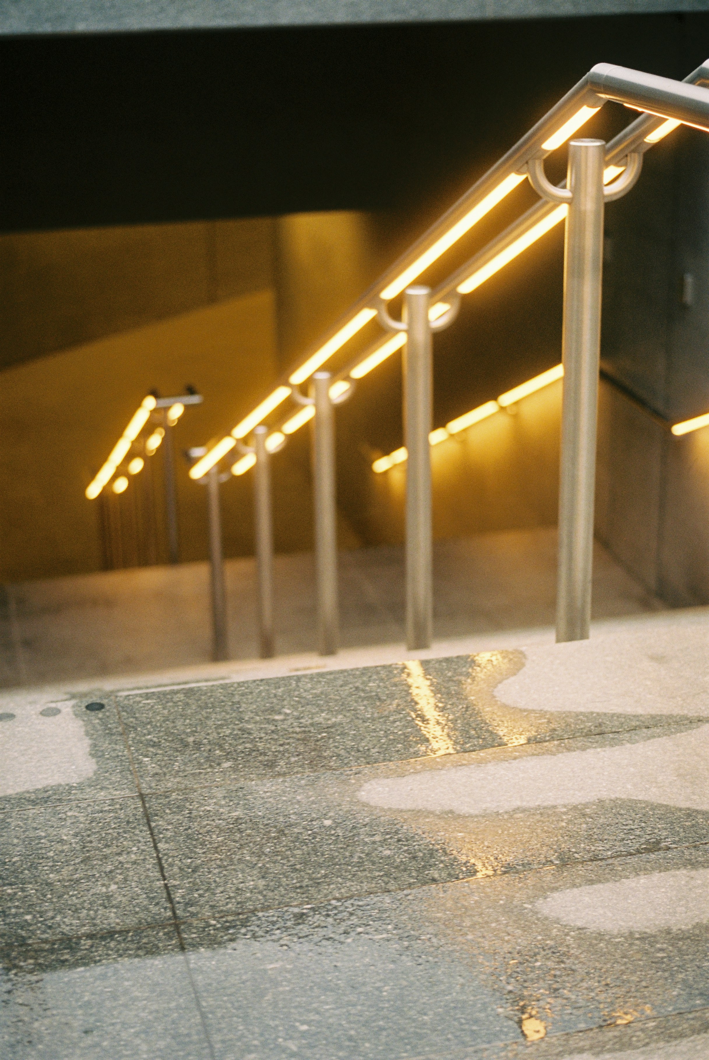 Stylish staircase with illuminated handrails and reflective wet surface, creating a contrast between light and shadow.
