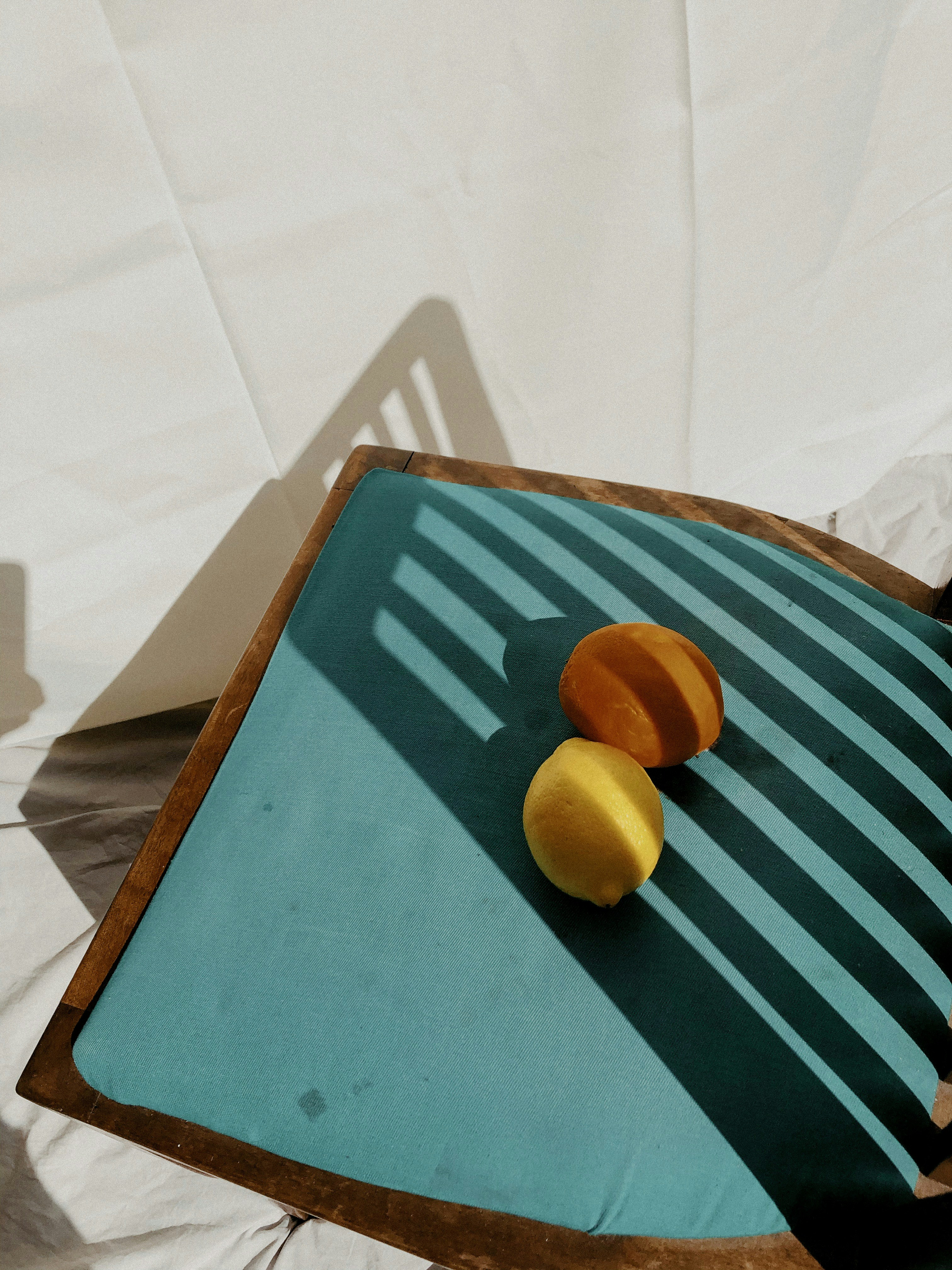Two vibrant citrus fruits resting on a teal surface, with playful shadows cast by slatted light. The composition highlights their colors and textures.